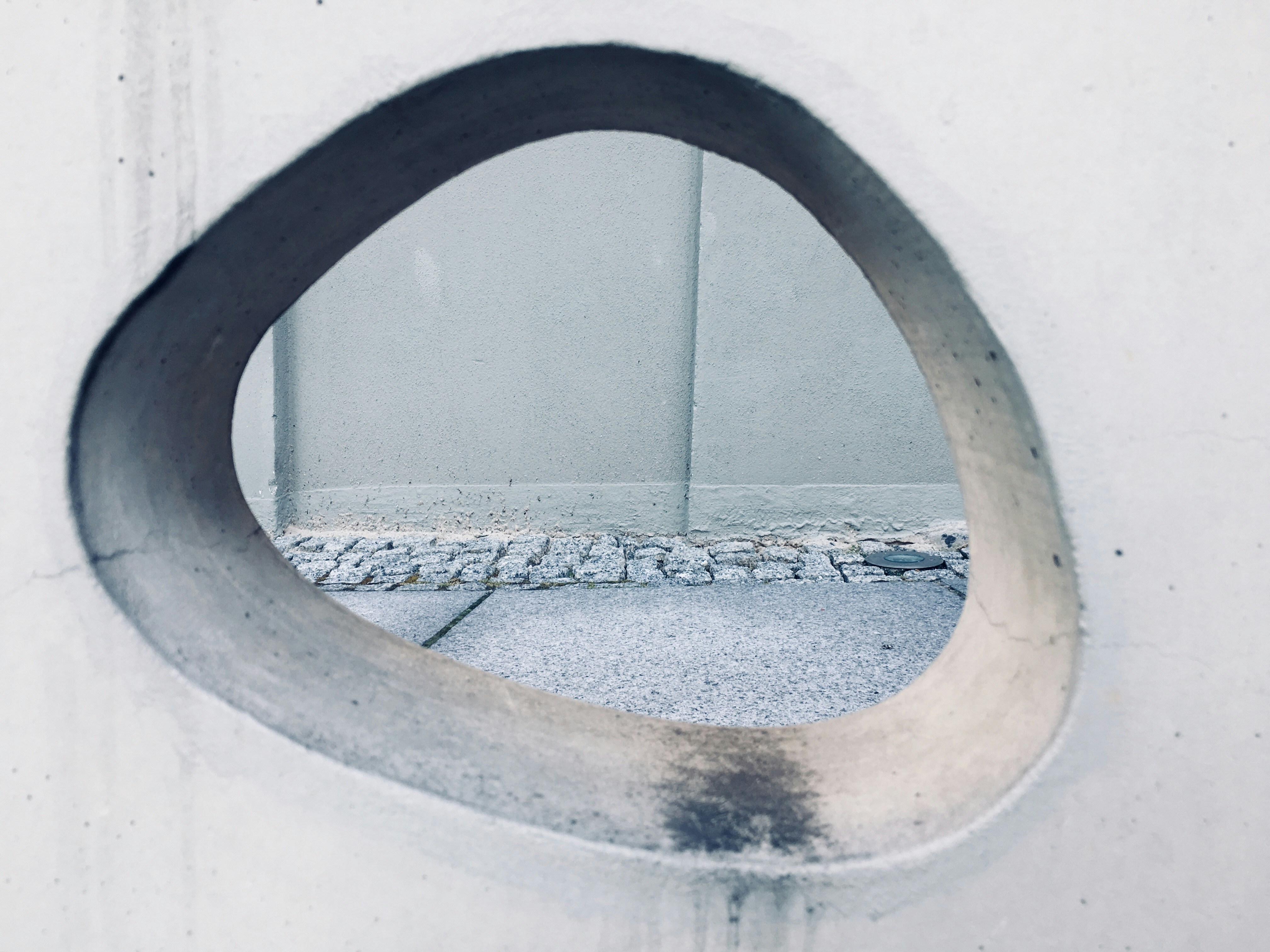 Circular aperture in a concrete wall: a portal to a quiet courtyard