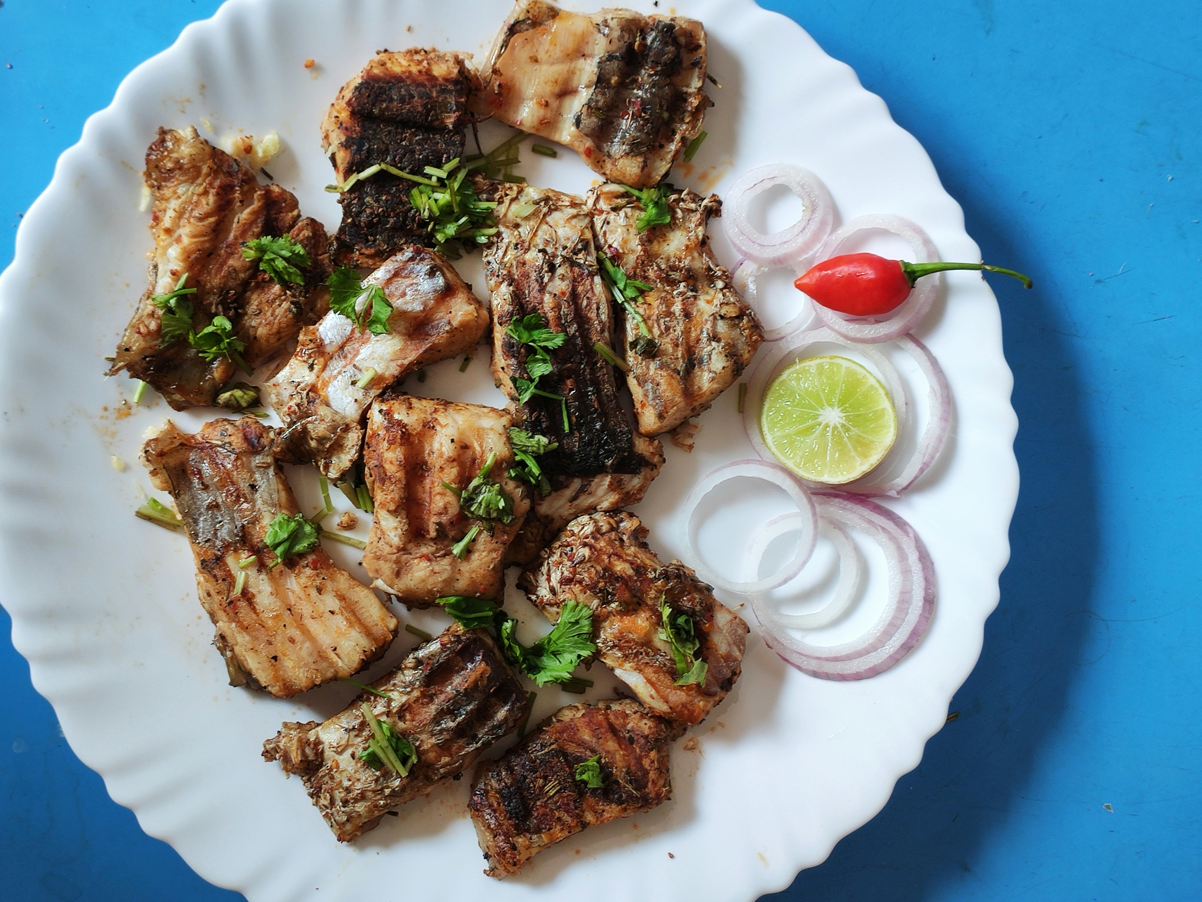 A platter of grilled fish garnished with fresh coriander, accompanied by sliced onions, lime, and a red chili. Perfectly arranged for an appetizing presentation.