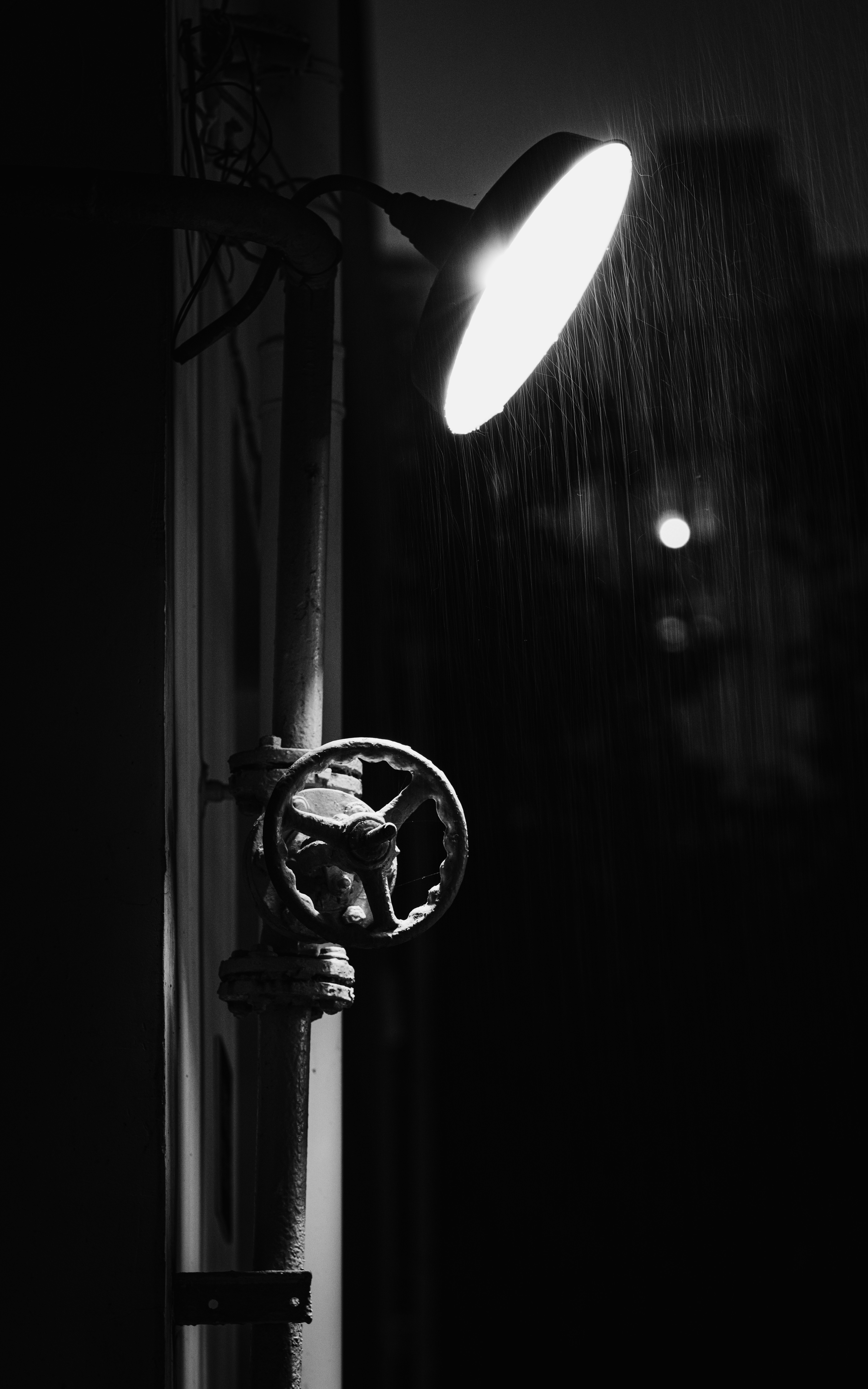 Industrial Light: Rain-Tipped Lamp Casting Shadows on a Valve
