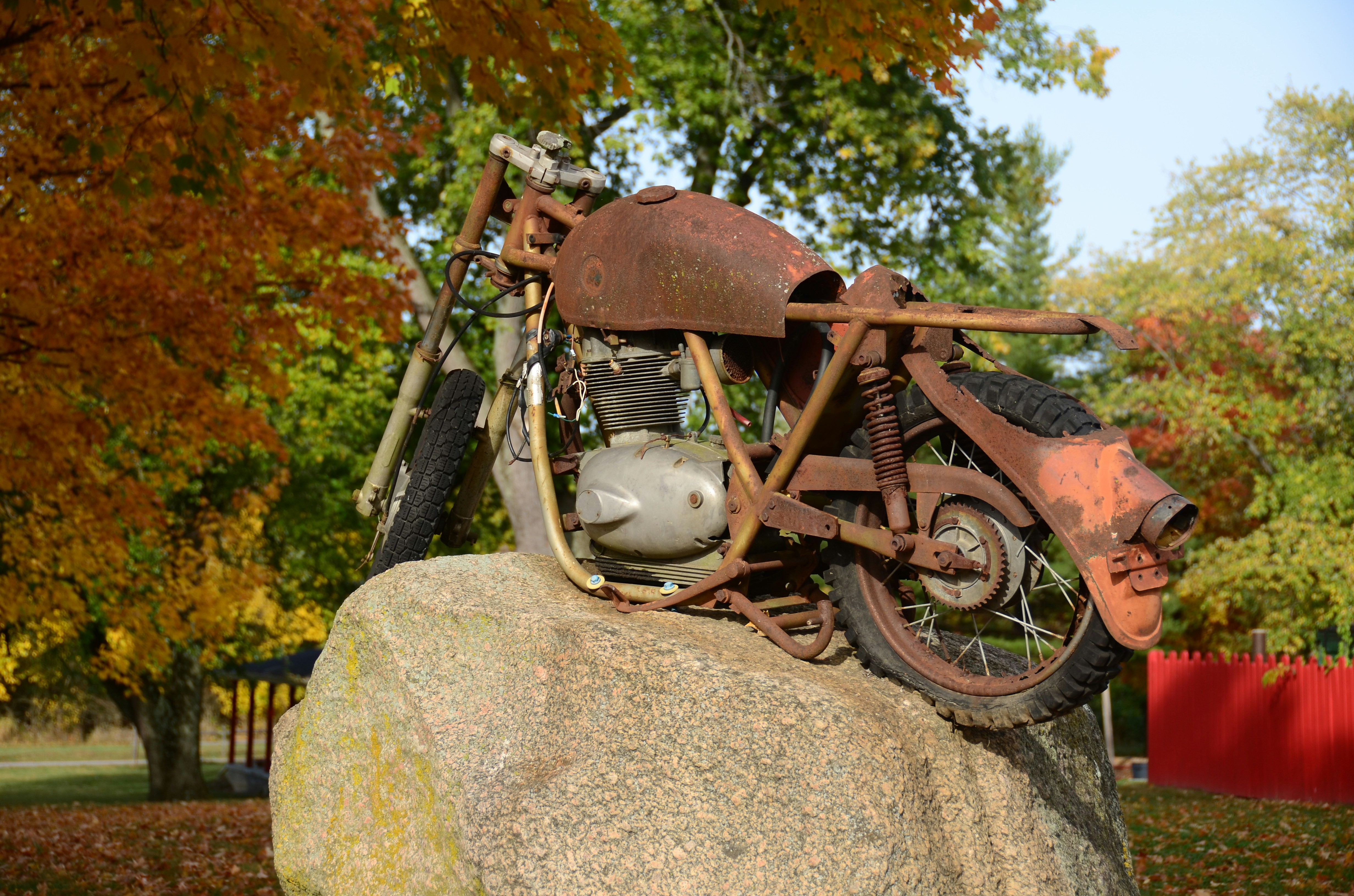 Rusting Ride: A vintage motorcycle perched atop a granite pedestal in autumnal light