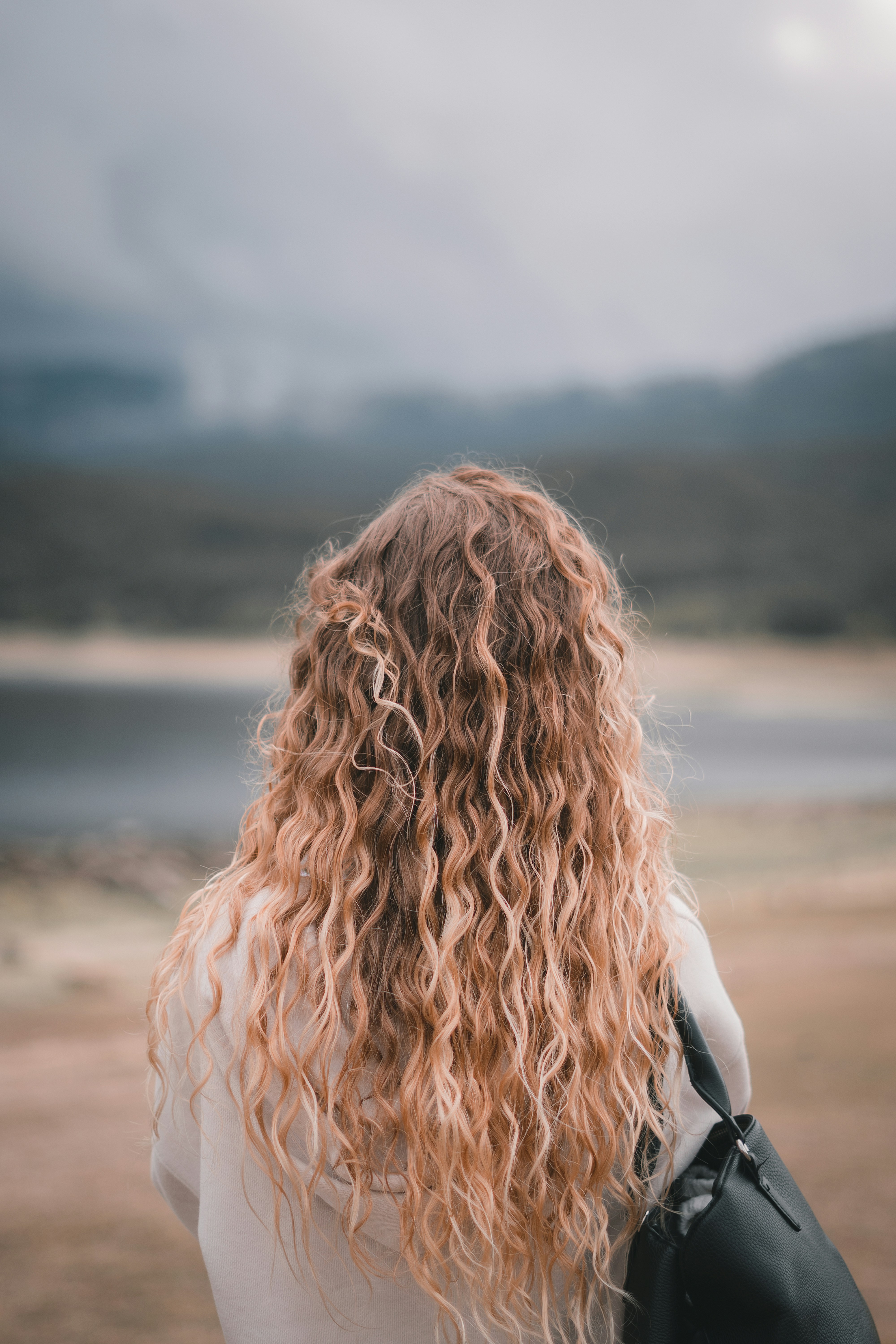 A woman with curly hair gazes out over a serene landscape, embodying tranquility against a moody sky.
