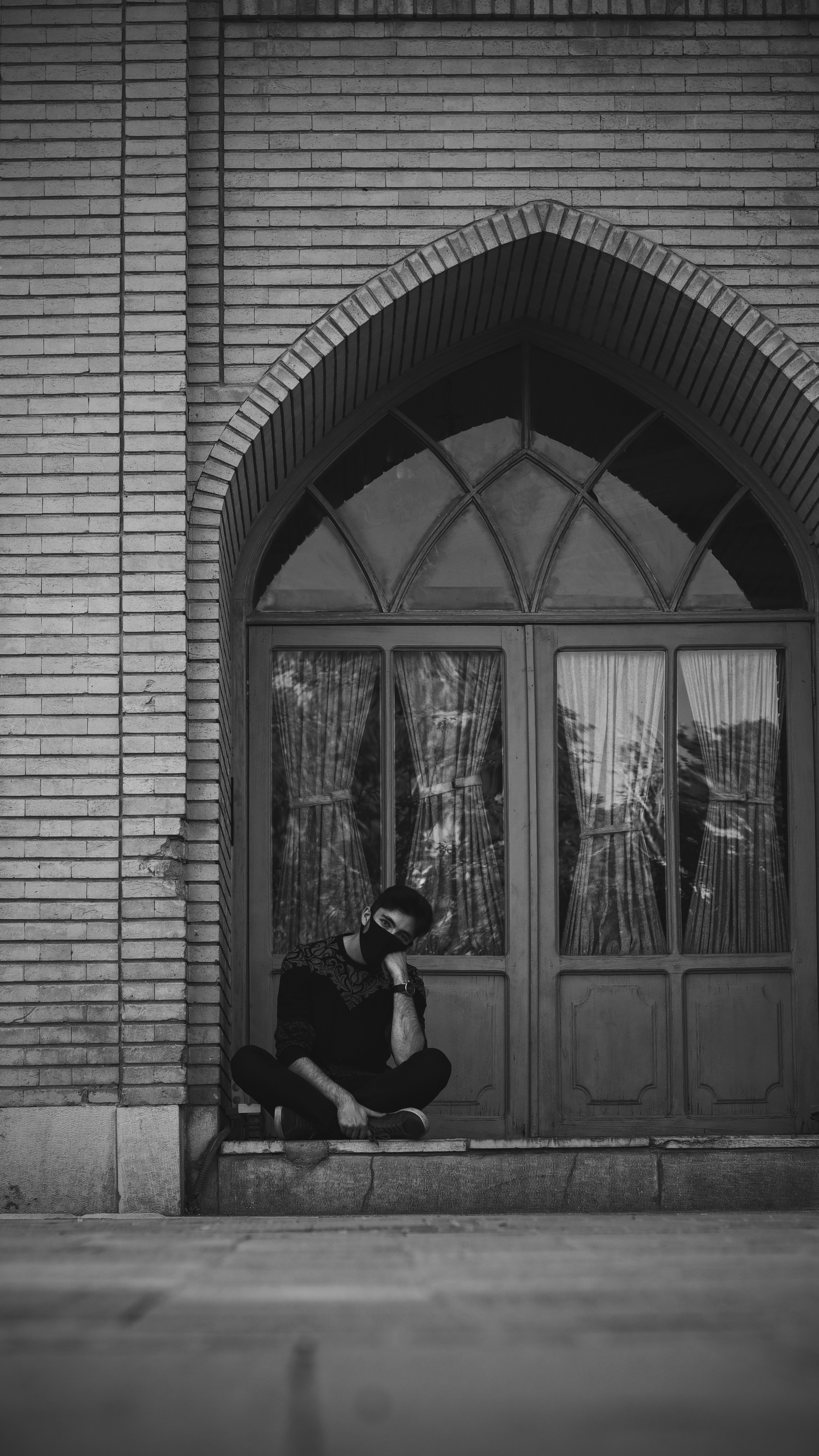 A solitary figure sits against a vintage doorway, lost in thought, with flowing curtains framing the scene. The monochrome palette enhances the mood of introspection.