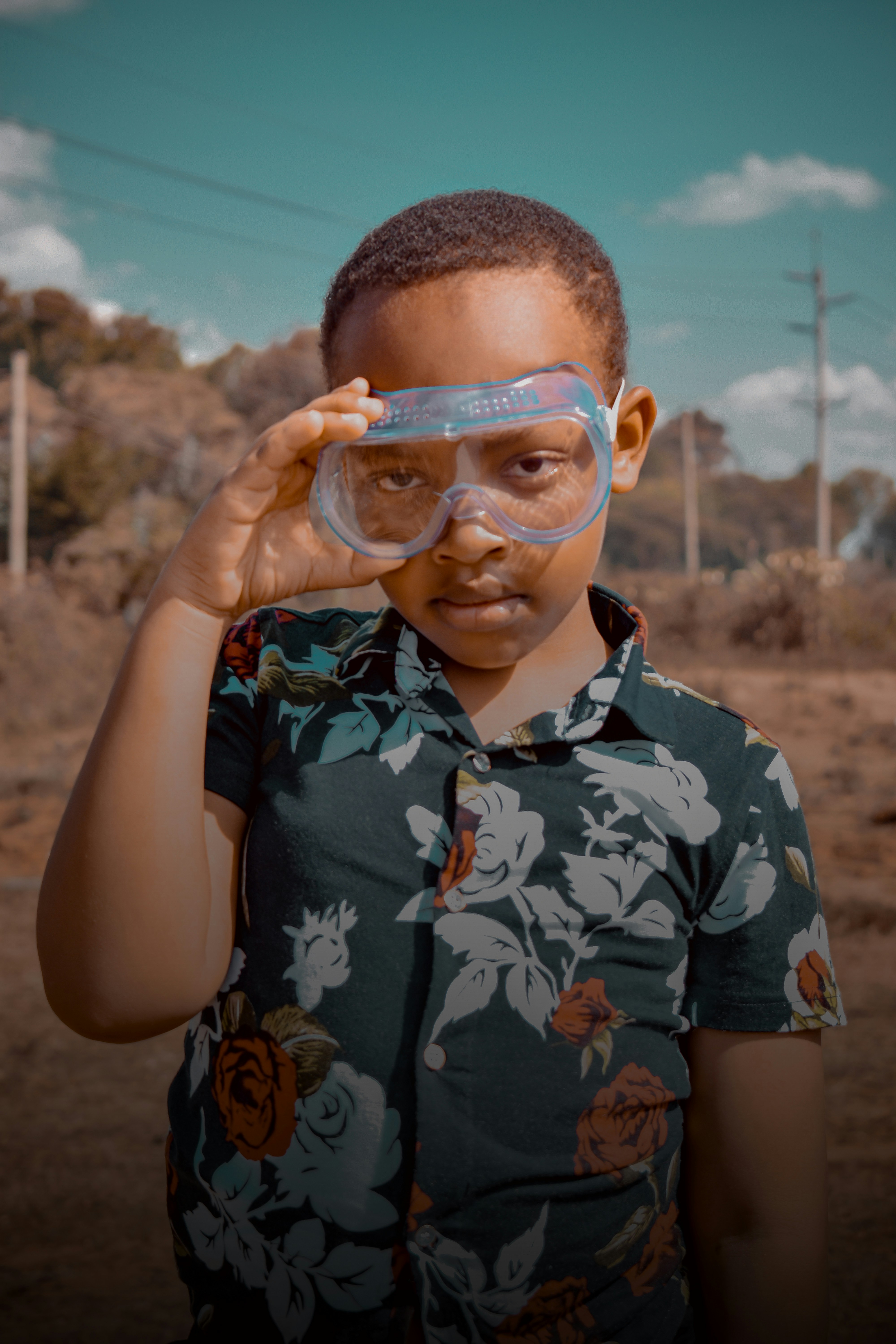 Goggles on, curiosity in focus: a sunlit portrait of a boy in a floral shirt