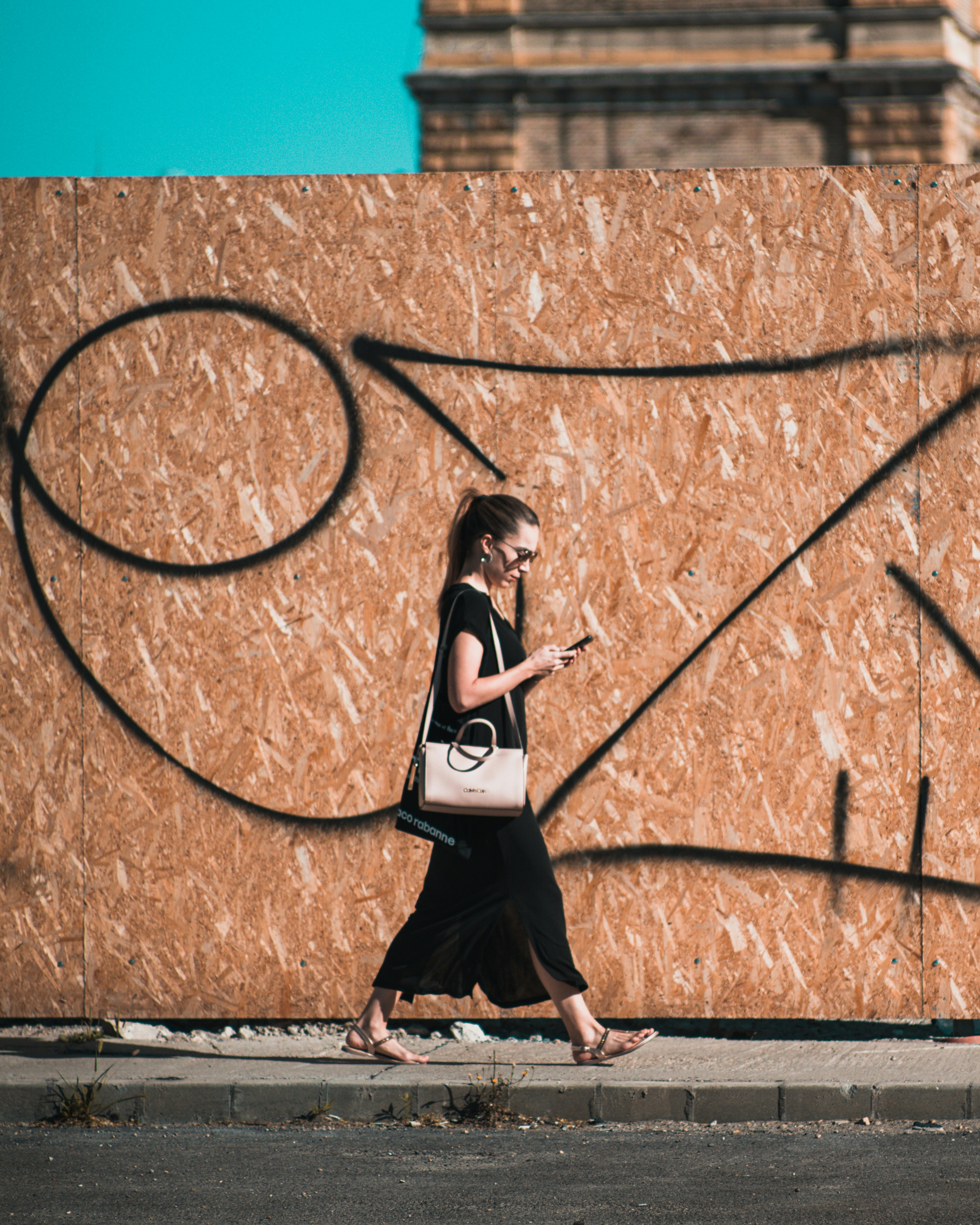 woman in black dress leaning on brown wall