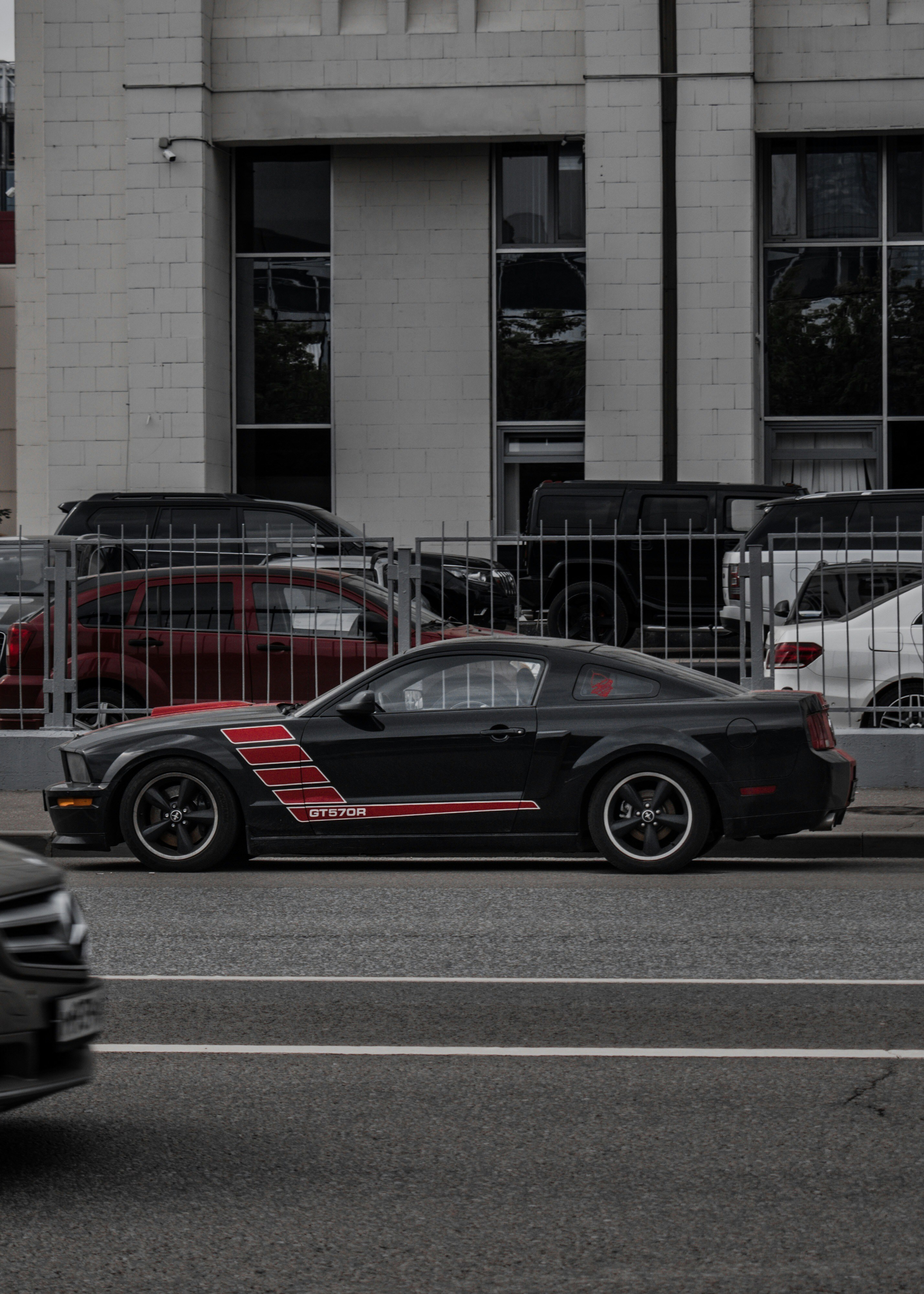 A sleek black sports car with red stripes parked along a city street, reflecting a blend of modern design and classic appeal.