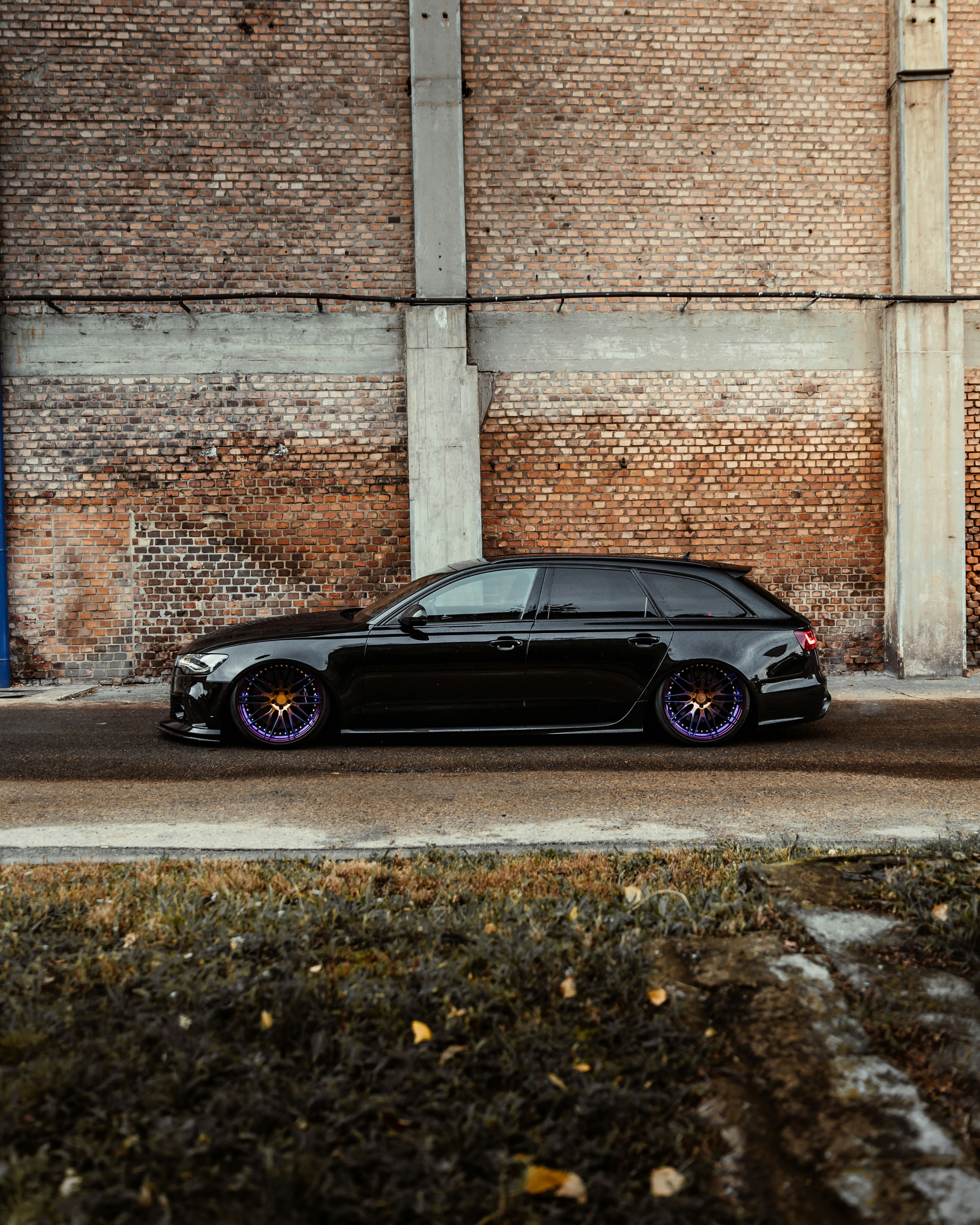 Low-slung black sedan with iridescent rims against a weathered brick wall