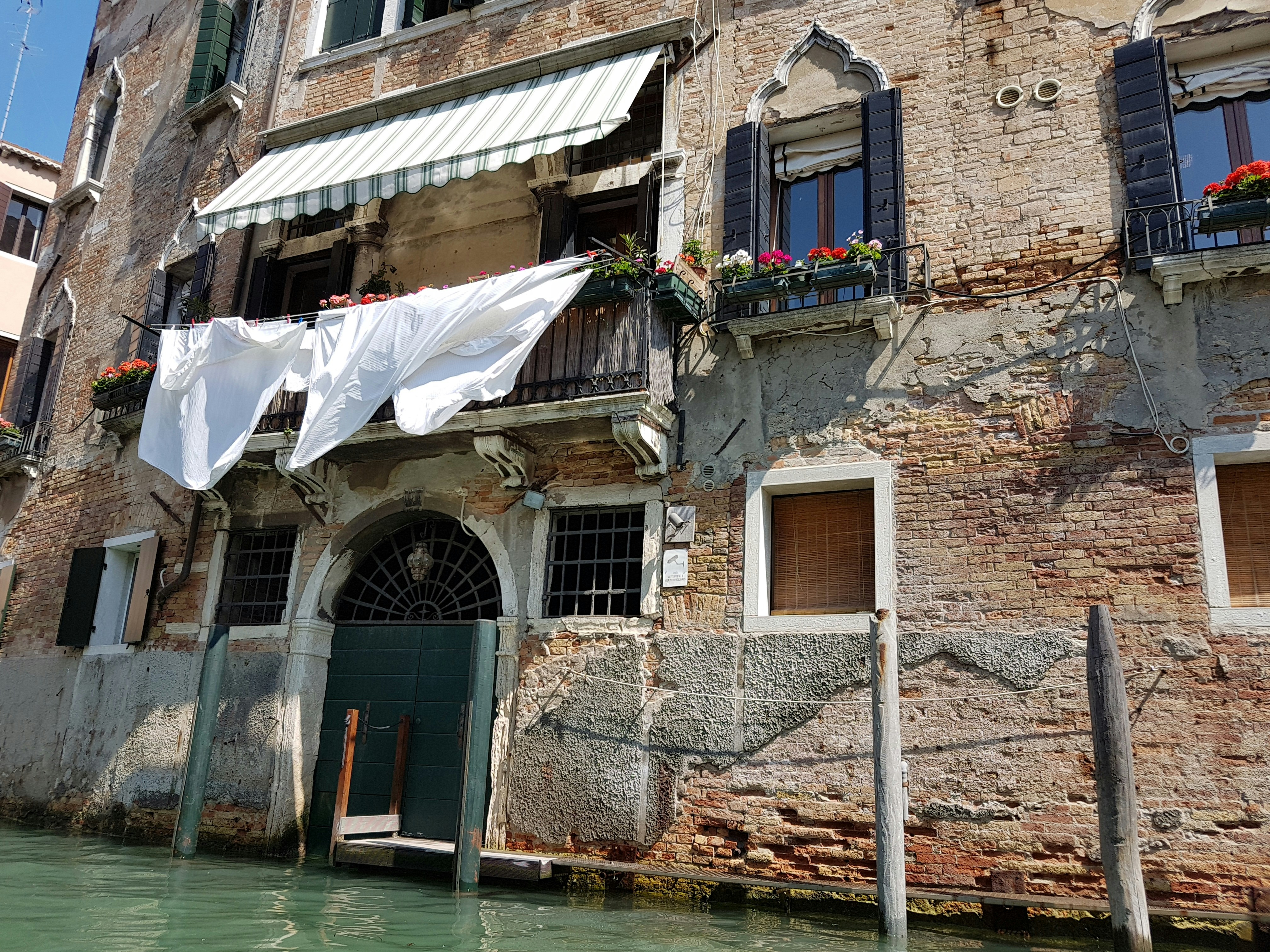 Weathered Venetian Facade: Arched Door, Balcony Blooms, and Laundry by the Canal