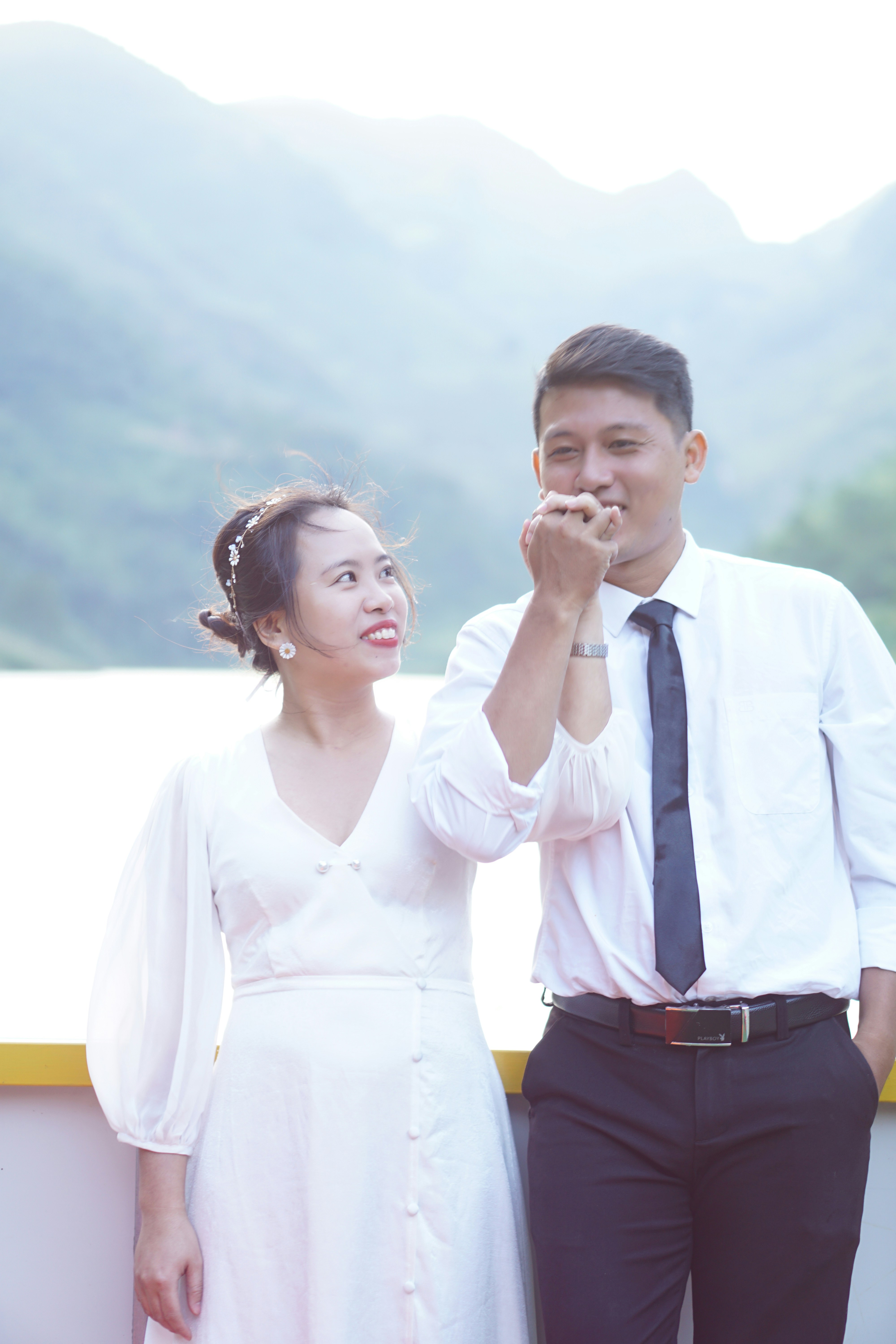 Couple sharing a tender moment by a serene lake, framed by lush mountains in the background.