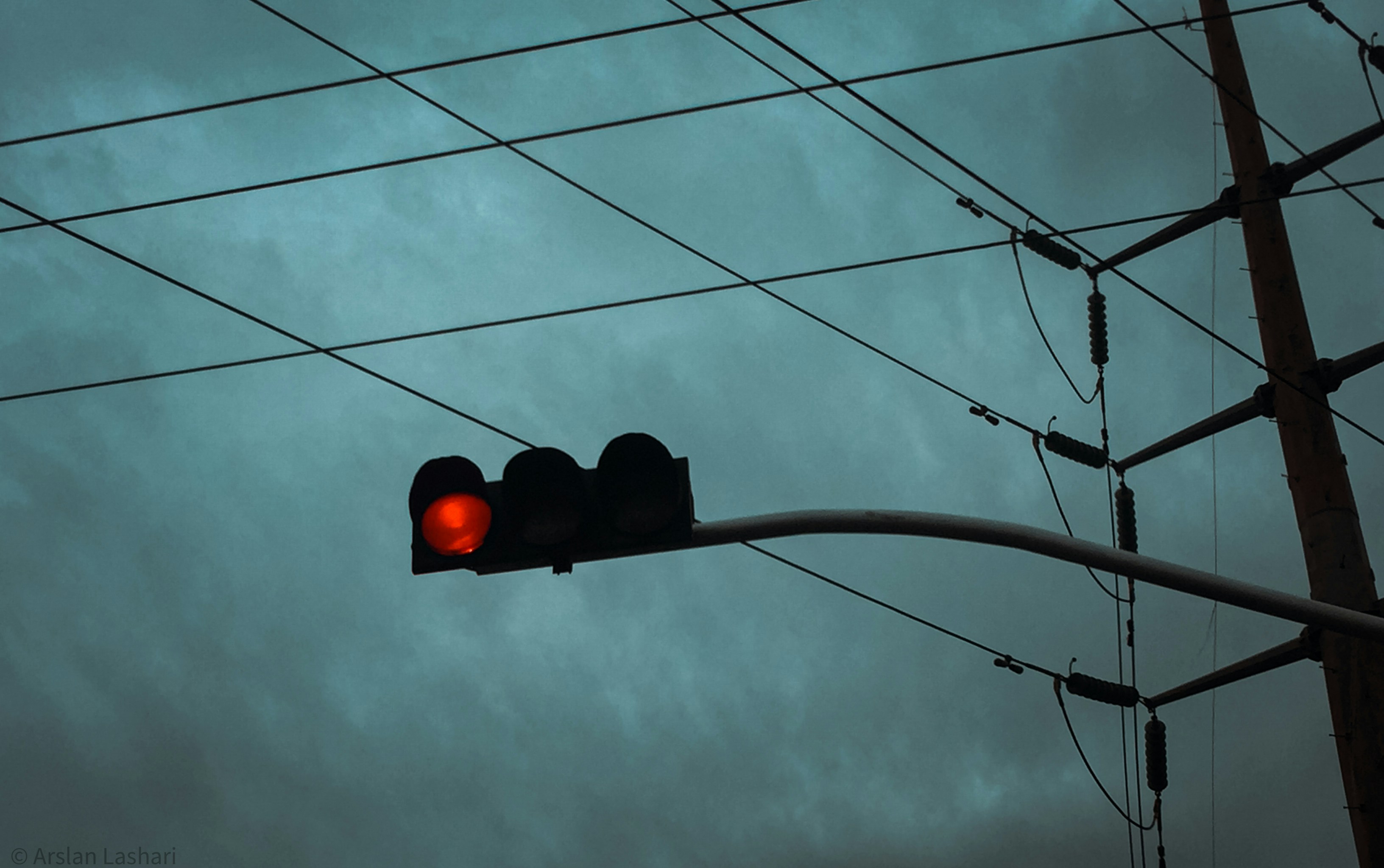 Traffic light glowing red against a backdrop of dark, overcast skies and silhouetted power lines.