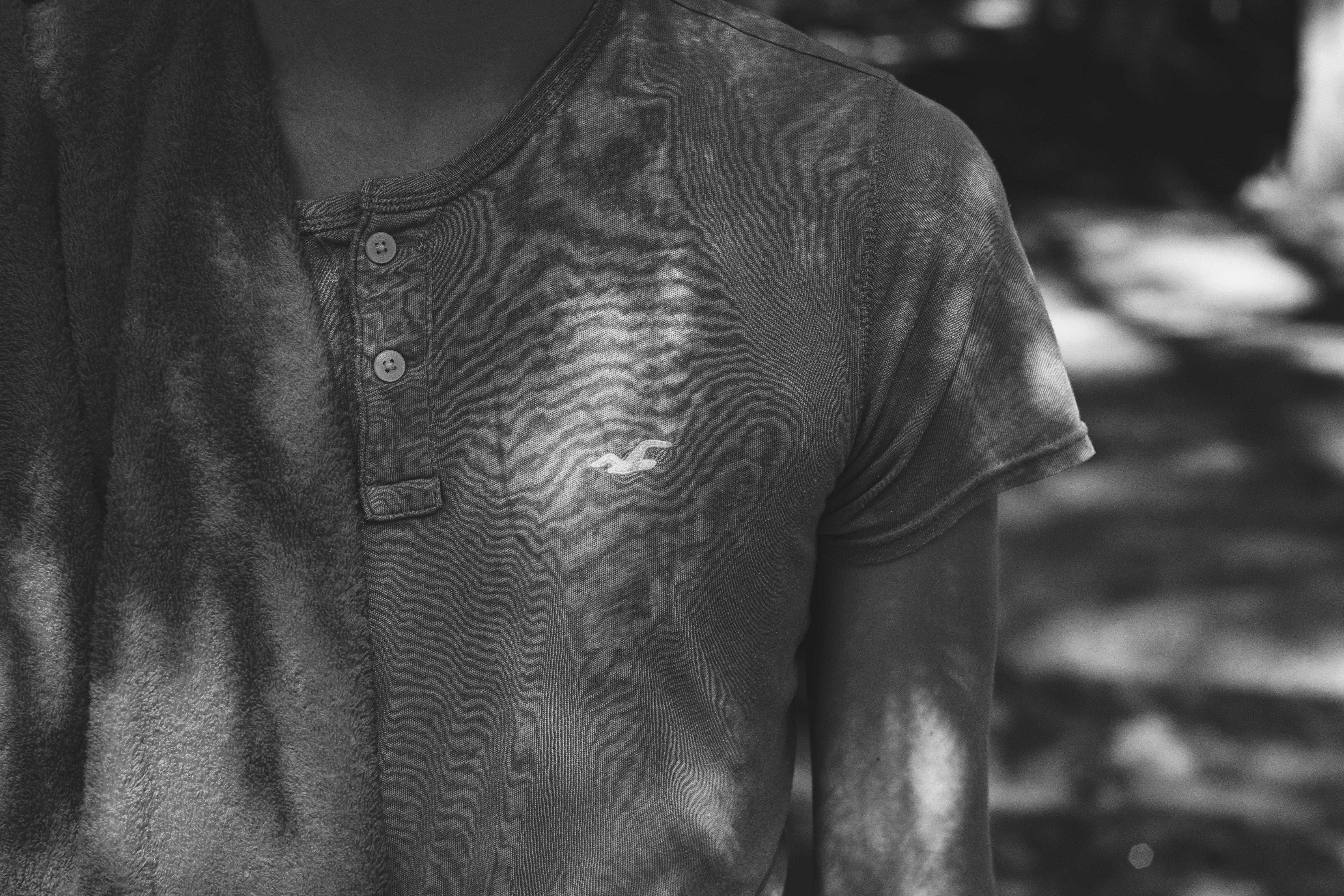 Close-up of a person wearing a short-sleeve shirt with sunlight filtering through tree leaves, casting shadows.