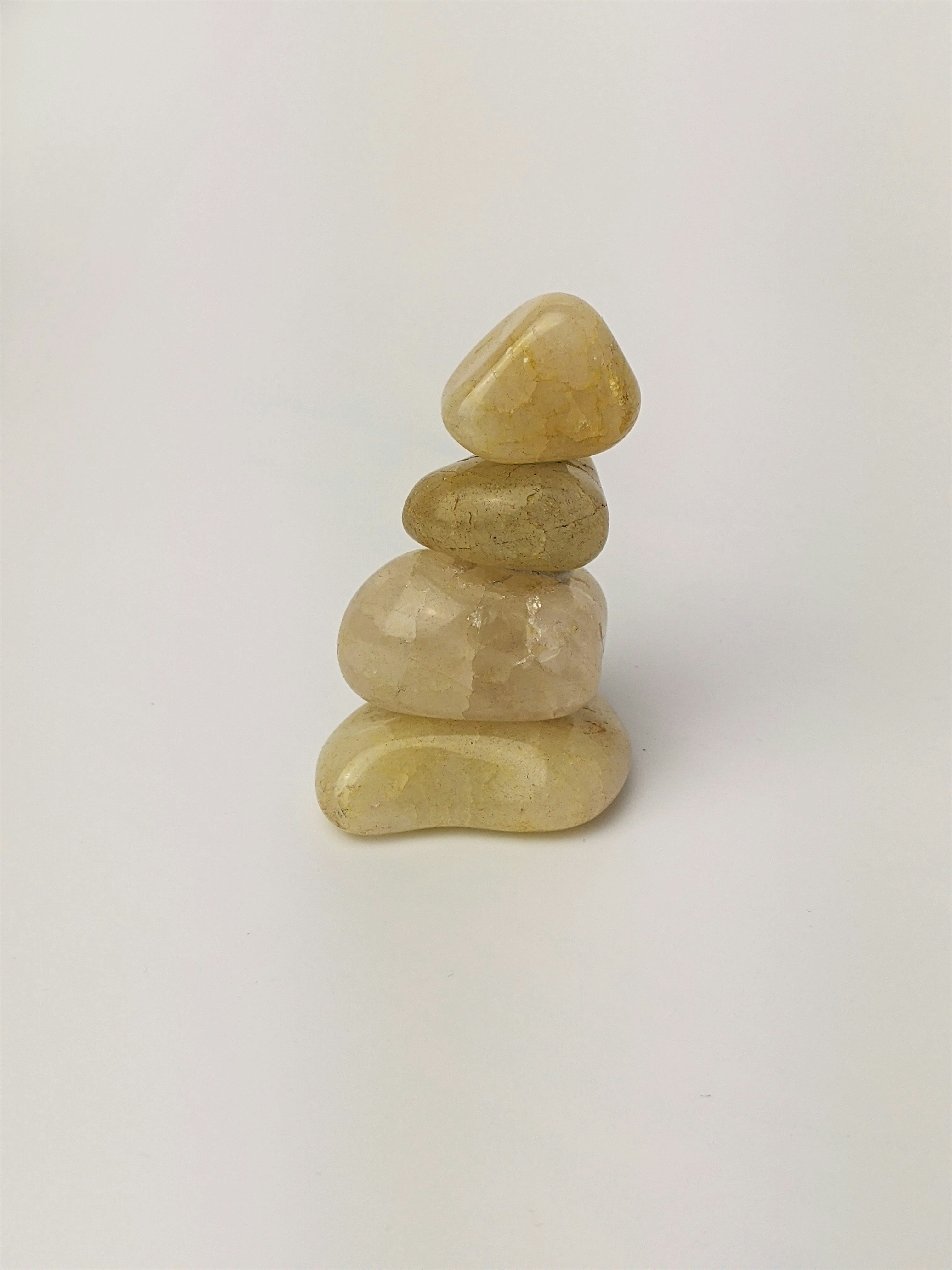 Four smooth, golden-hued stones stacked in a balanced formation against a soft white background.