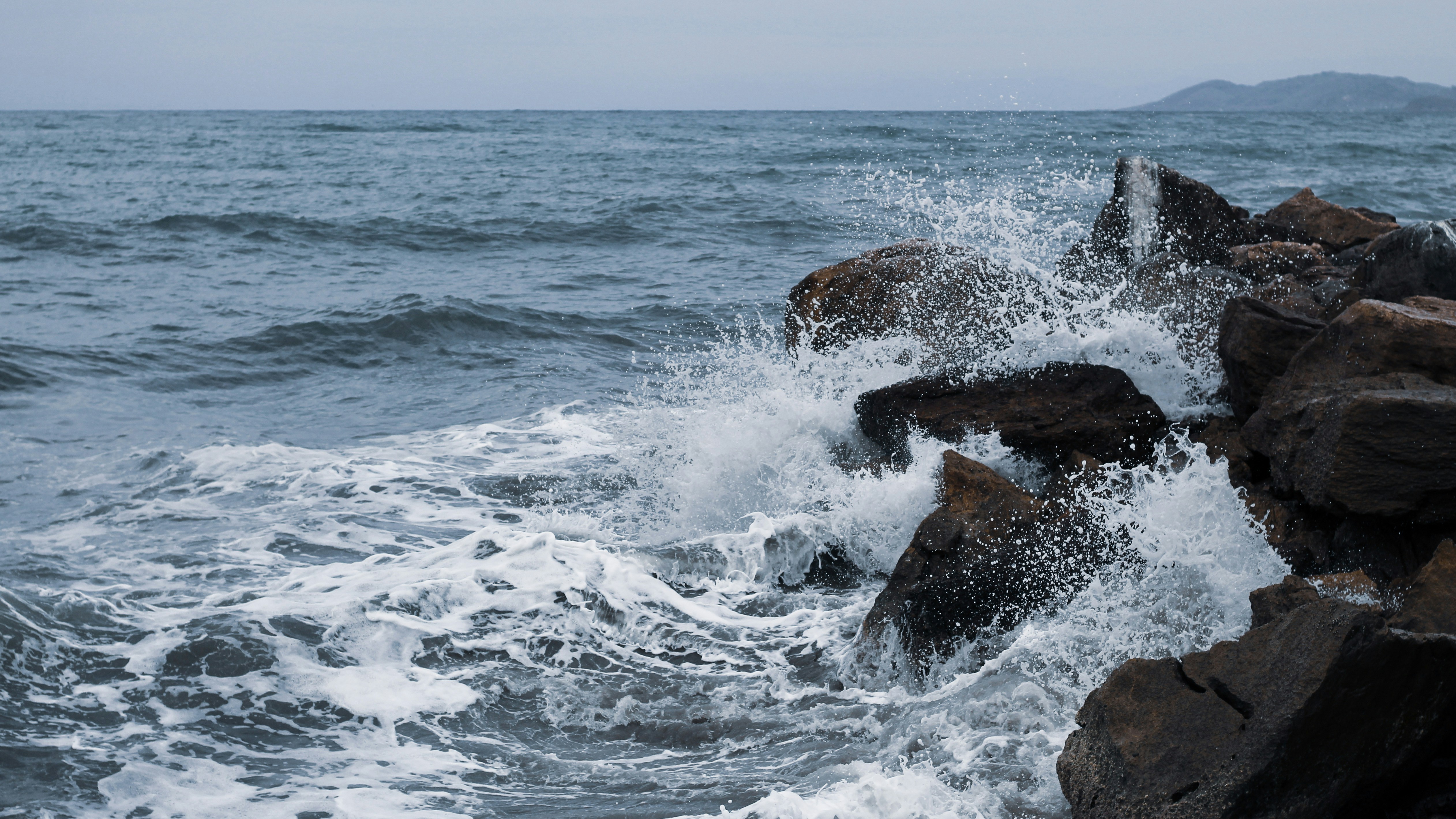 Waves crashing against rocky shoreline under a cloudy sky.