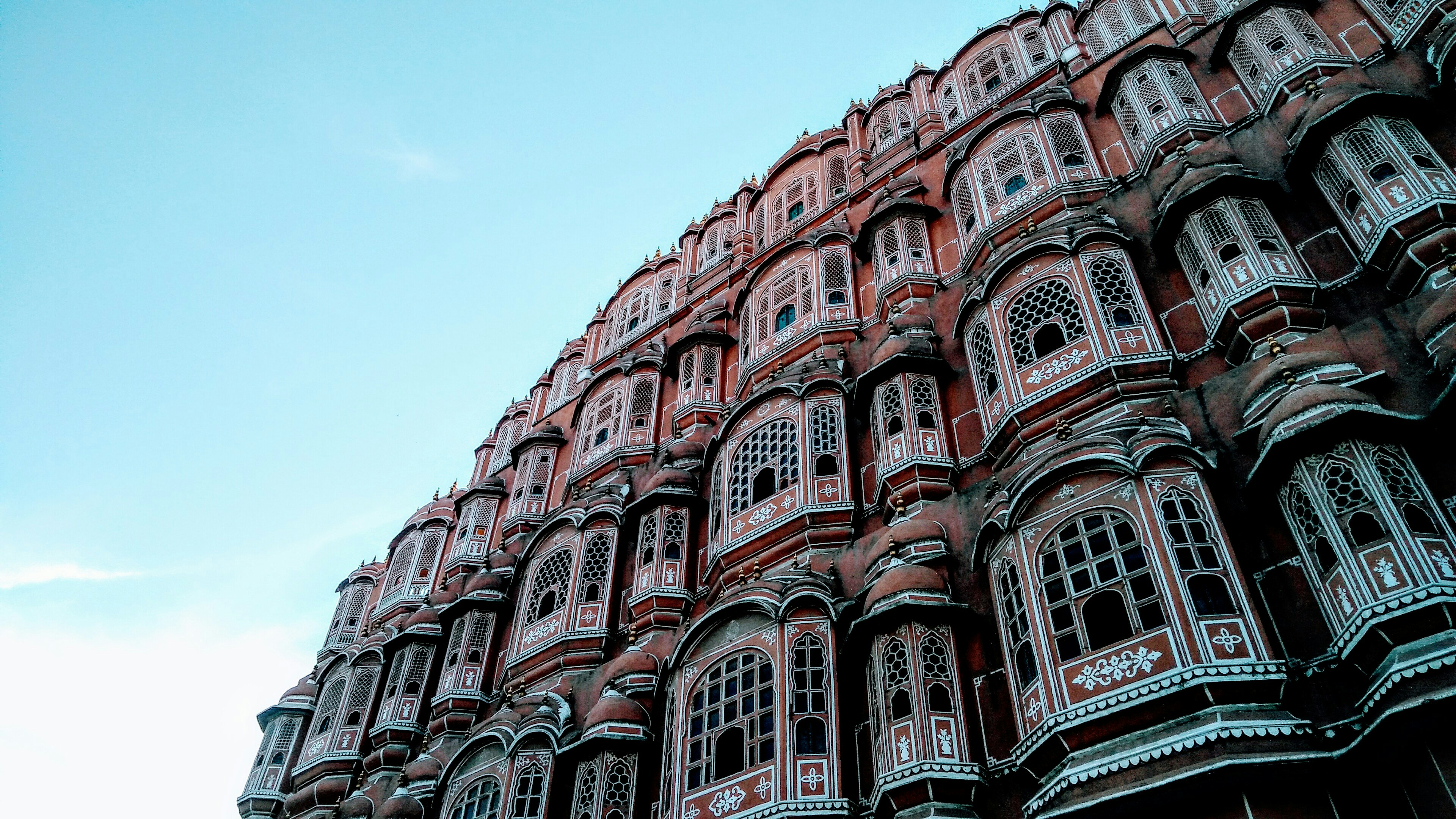 Close-up of an ornate red sandstone façade densely lined with arched lattice windows, rising toward a pale blue sky.