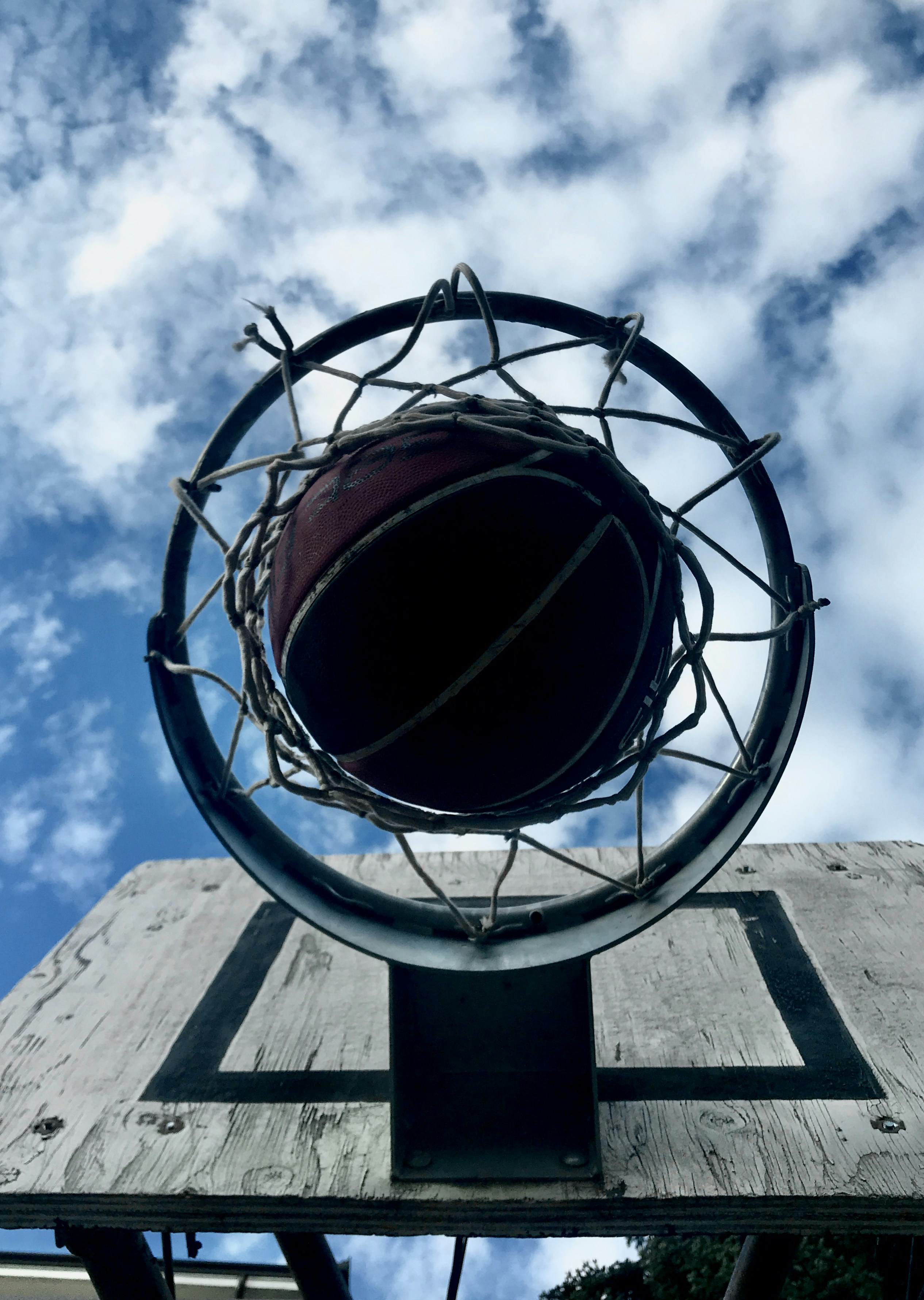 Basketball hoop framed against a backdrop of blue sky and scattered clouds, showcasing the ball poised for a perfect shot.