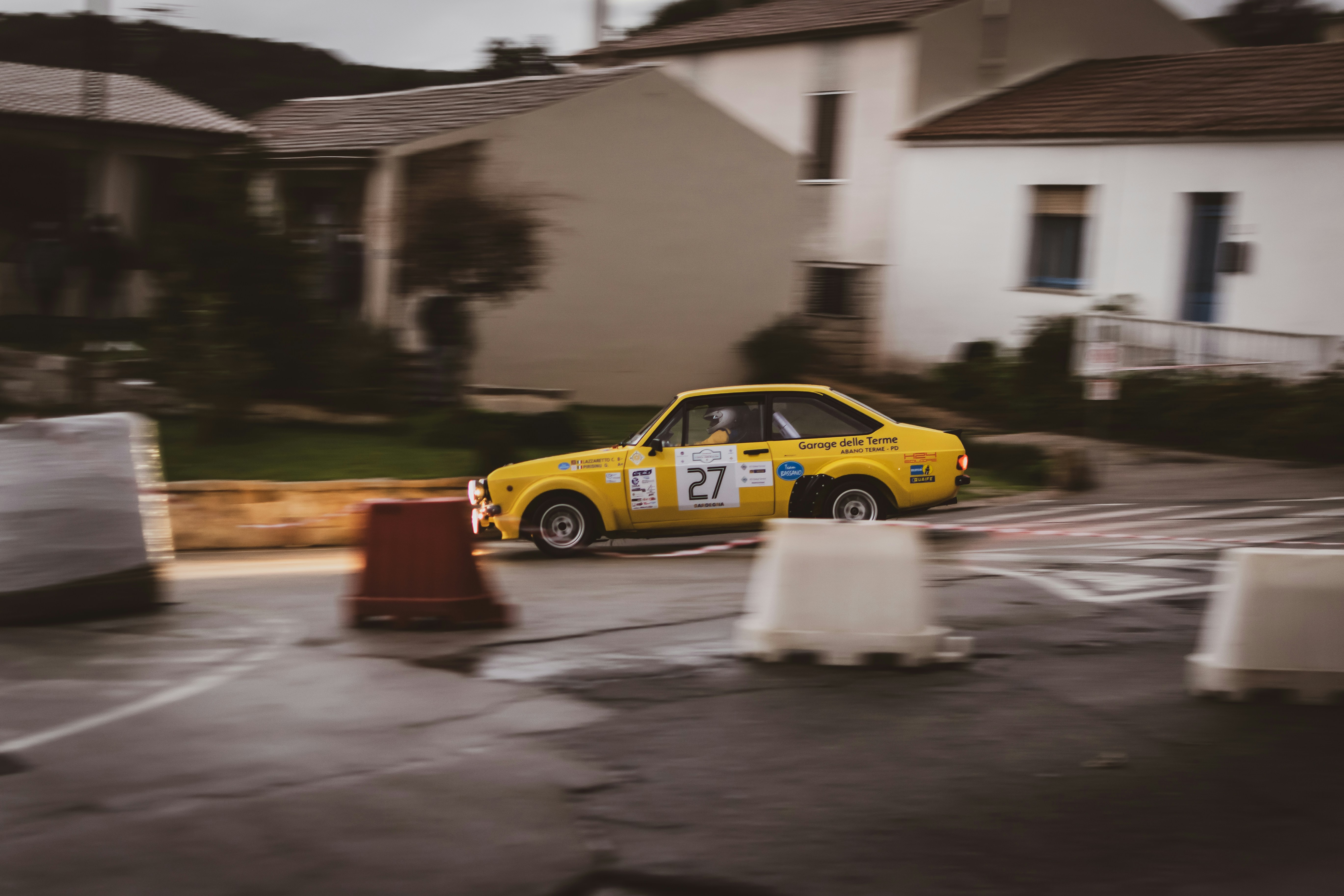 Yellow classic car racing past blurred barriers on a residential street.