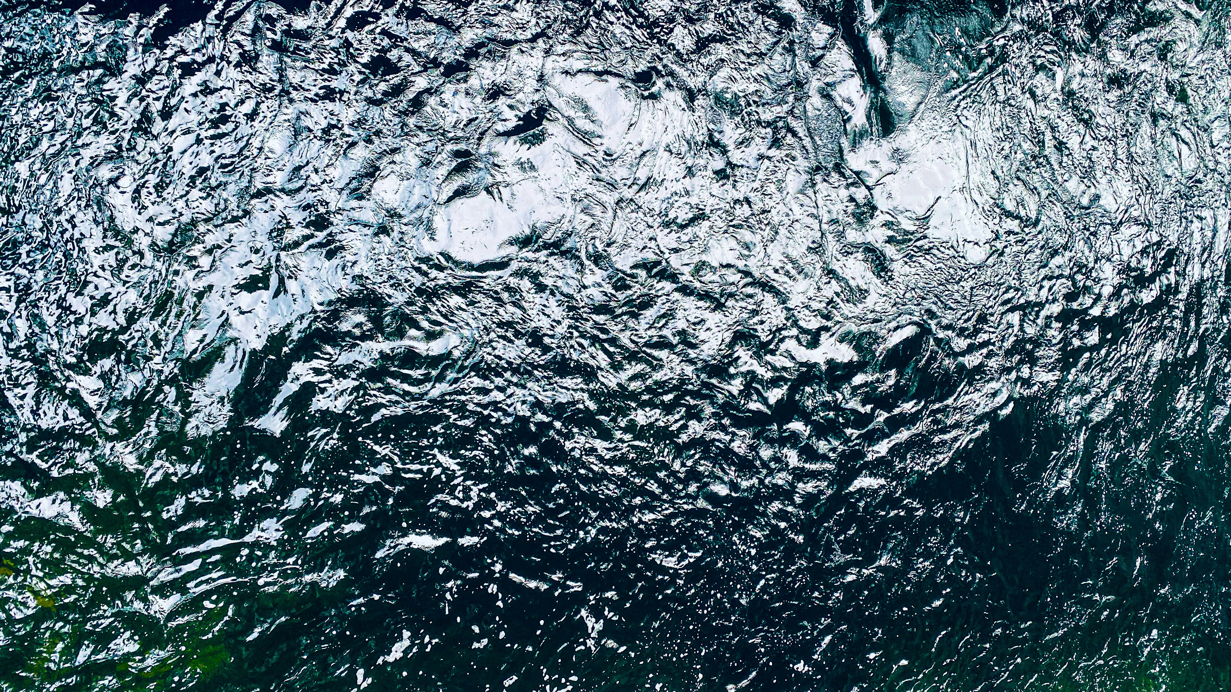 Dynamic surface of water reflecting sunlight, showcasing intricate patterns and textures. The scene captures the essence of natural fluidity.