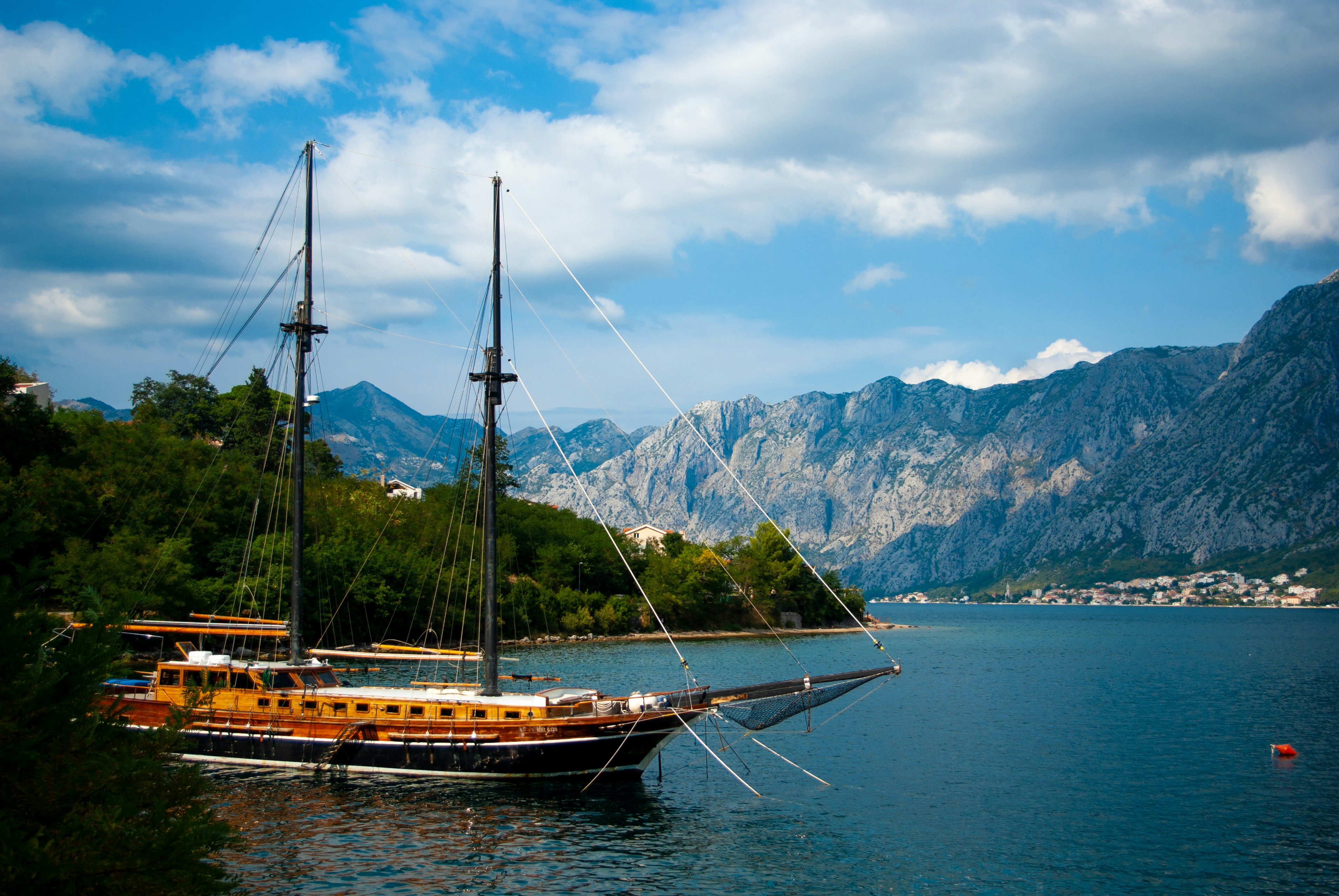 brown and white boat on sea near mountain under white clouds and blue sky during daytime
