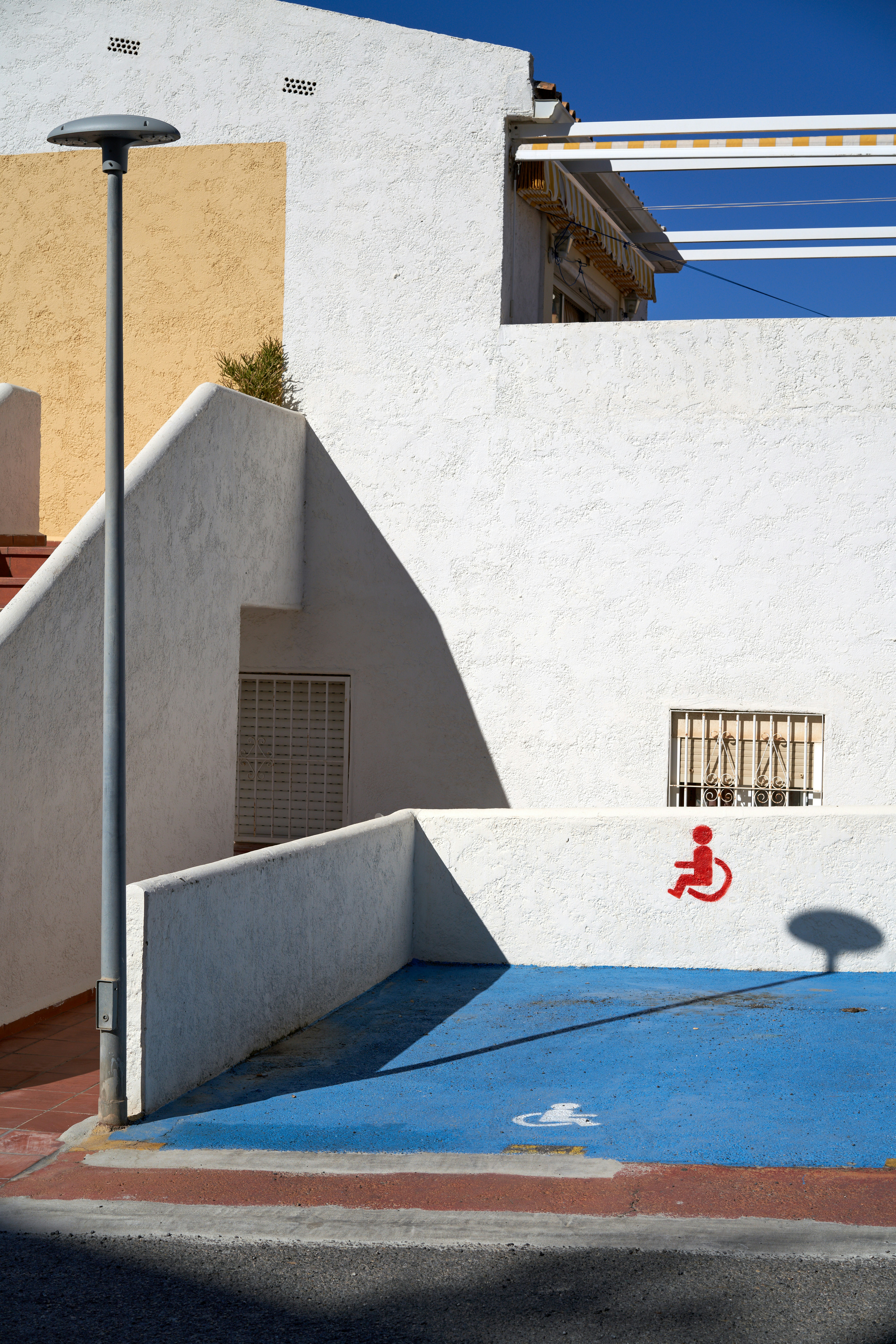 A blue parking spot designated for accessibility, featuring a red symbol on a white wall. The interplay of light and shadow creates a striking contrast.
