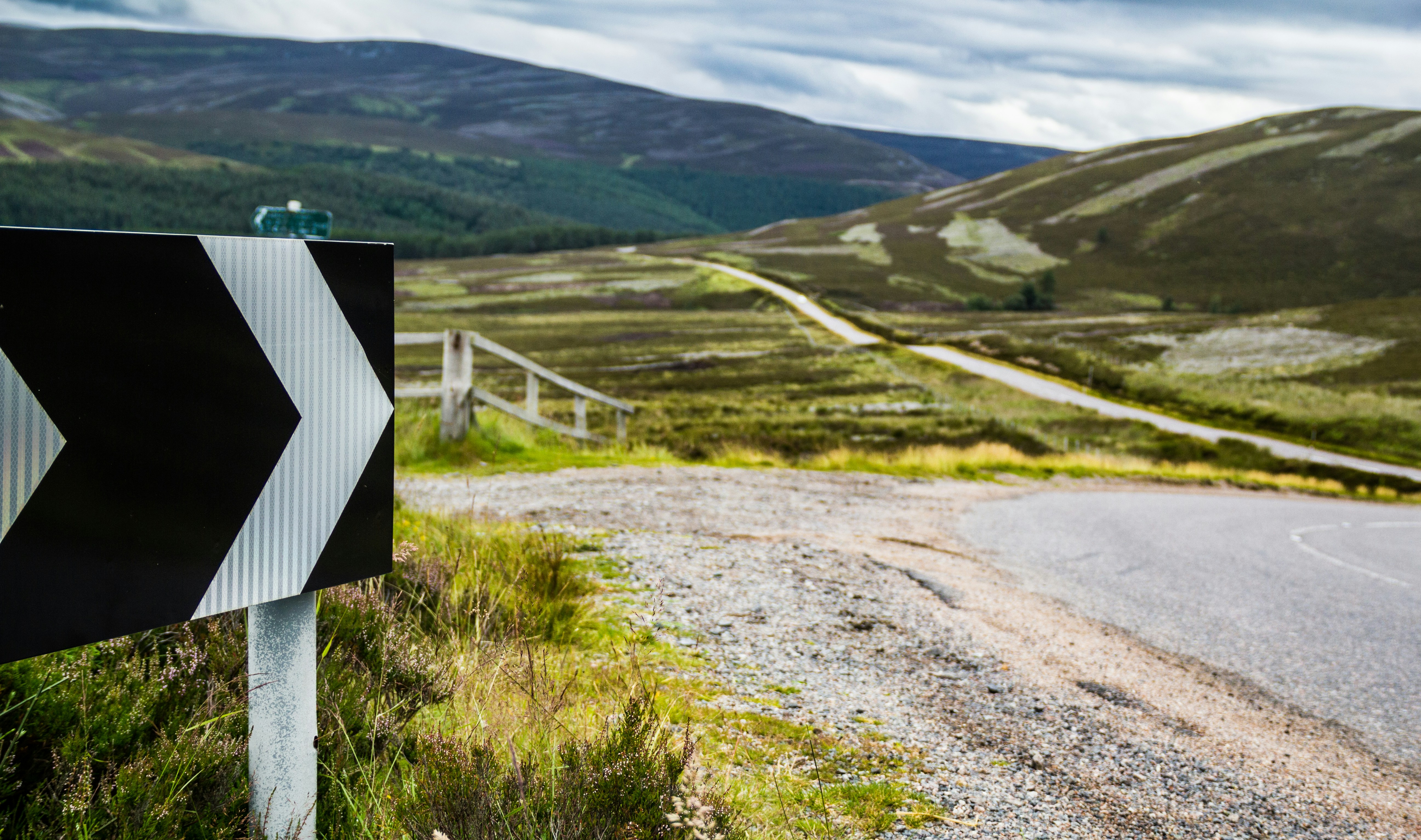 Curved road sign indicating a turn, set against a backdrop of rolling hills and expansive landscapes. The scene captures the essence of rural exploration.