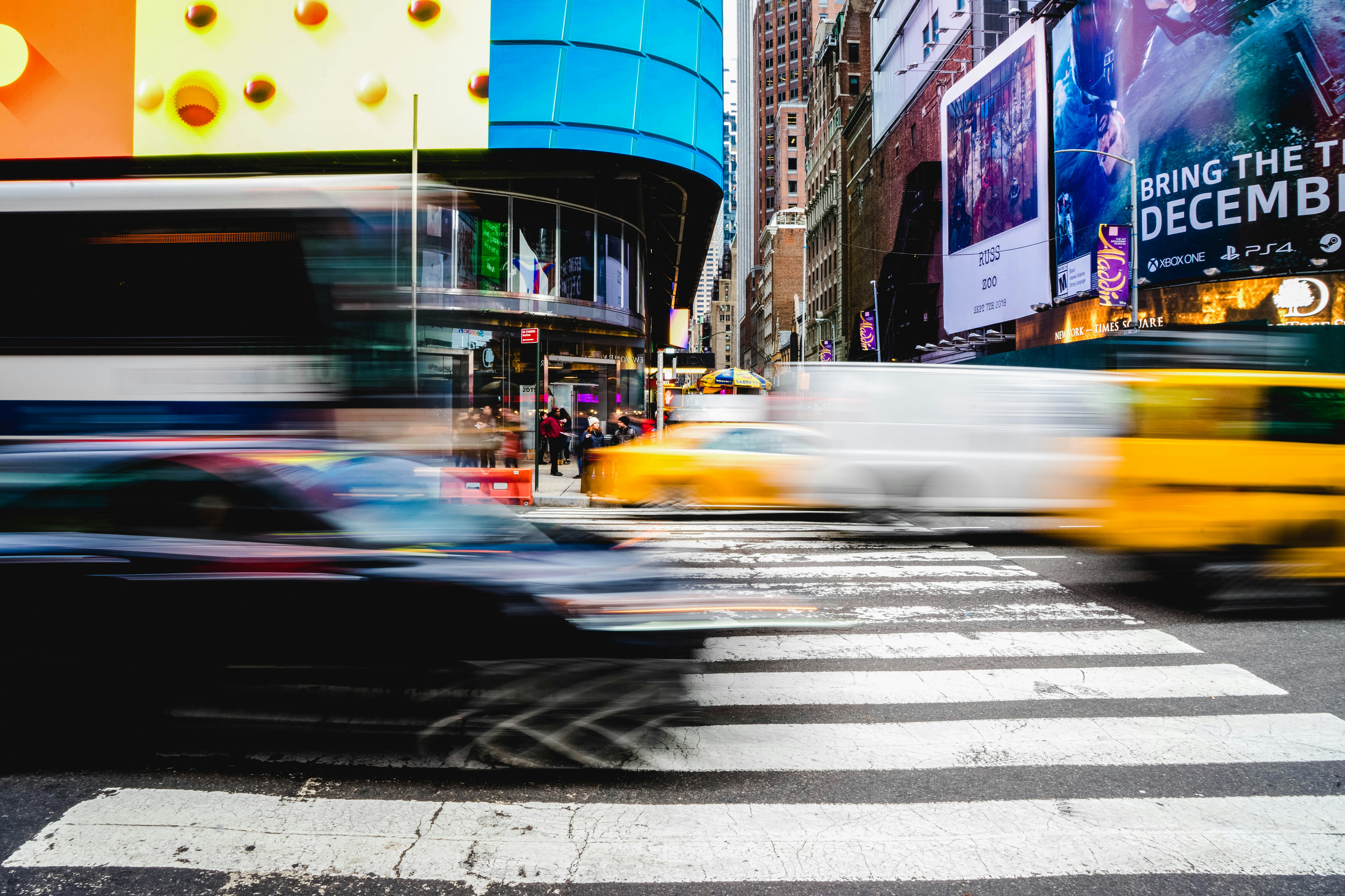 Dynamic scene of bustling traffic and pedestrians crossing a busy intersection in Times Square, showcasing vibrant billboards and city life.
