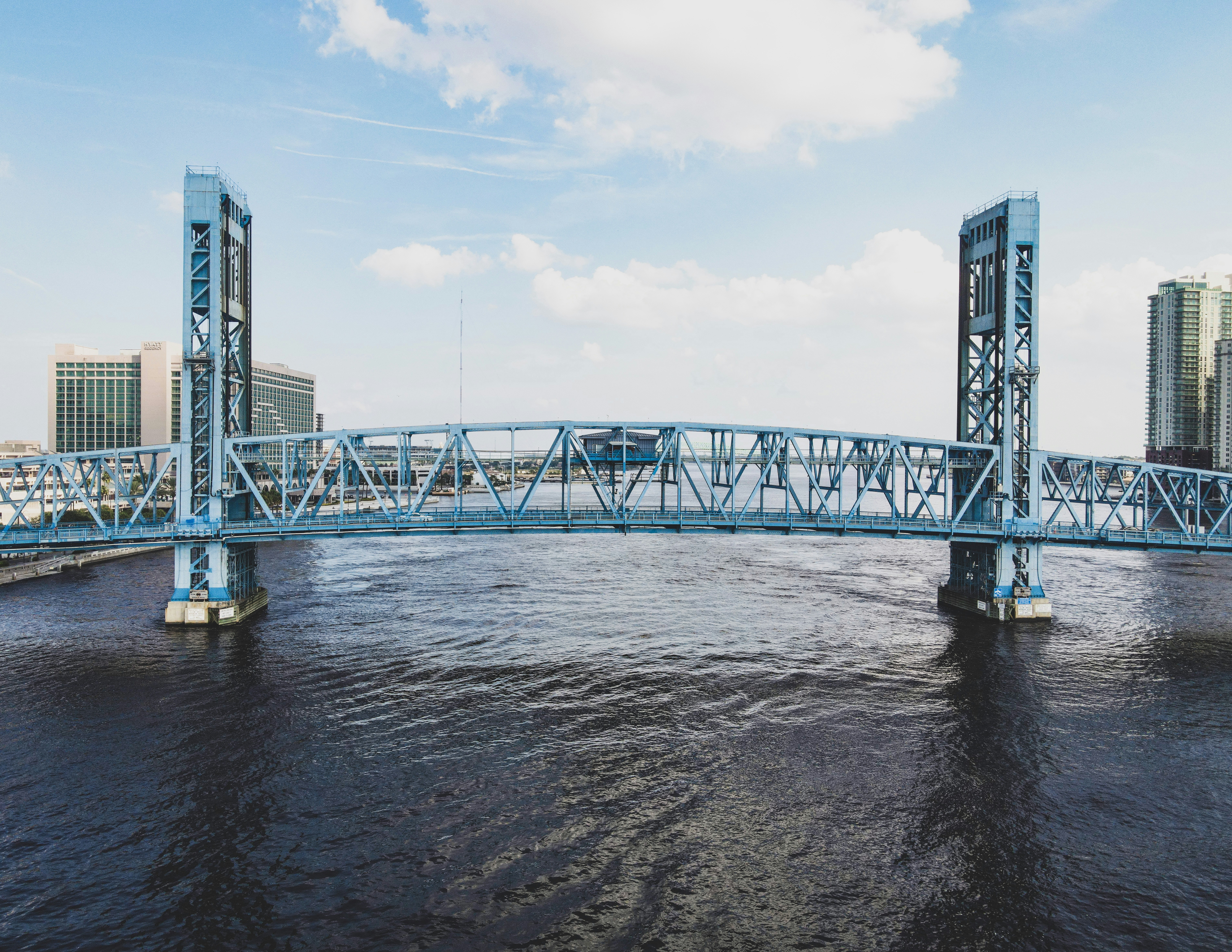 Blue steel drawbridge spanning a wide river with cityscape in the background.