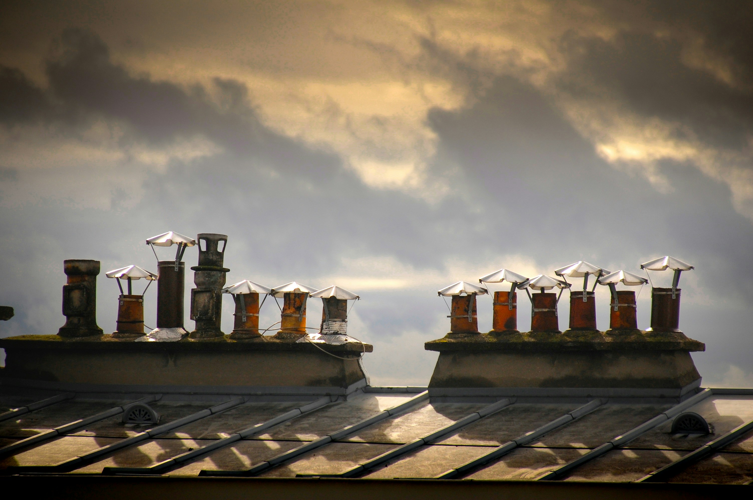 Chimneys adorned with glass caps line a rooftop against a dramatic sky, showcasing intricate architectural details.