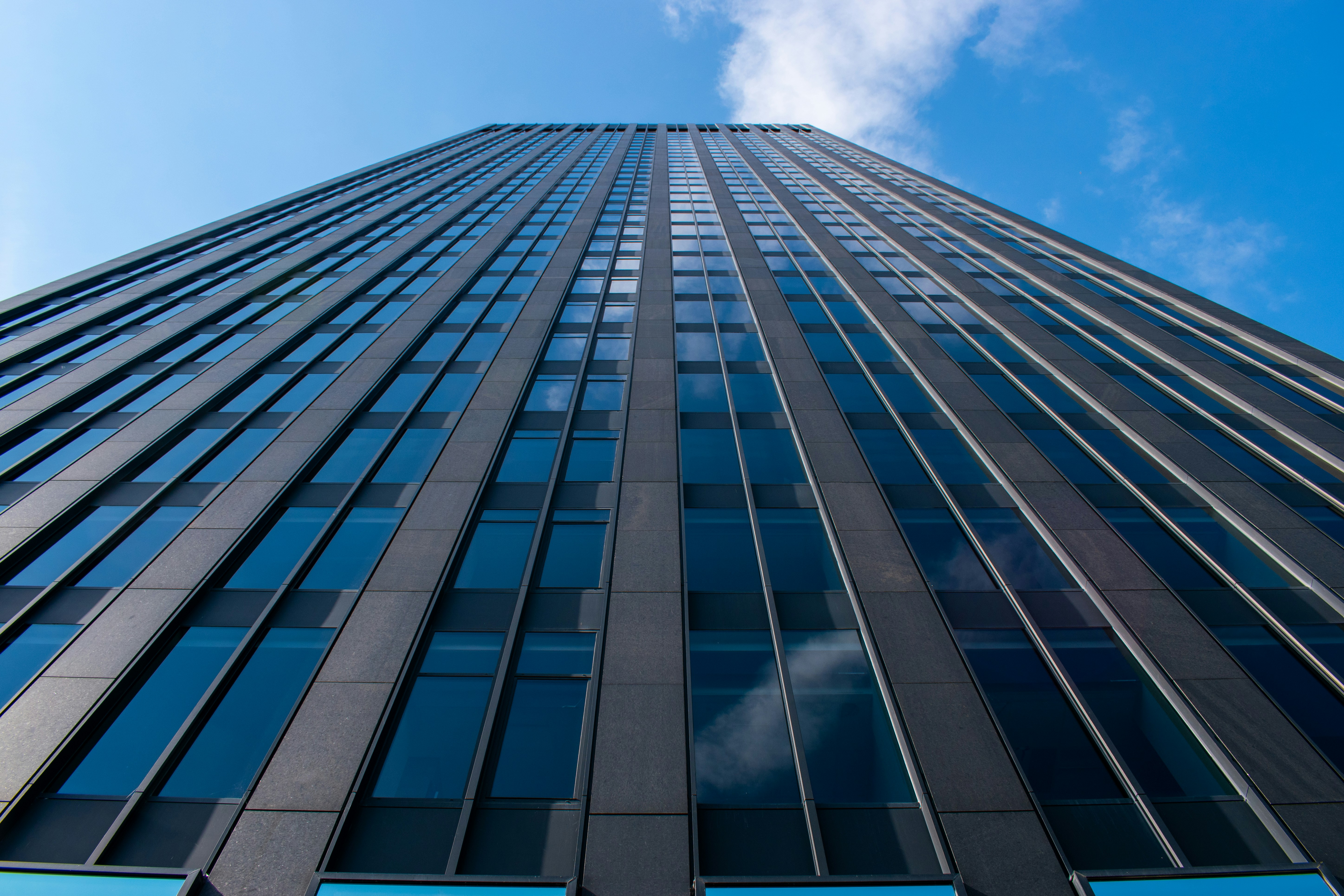 Tall skyscraper reaching towards a clear blue sky, reflecting clouds on its glass facade.