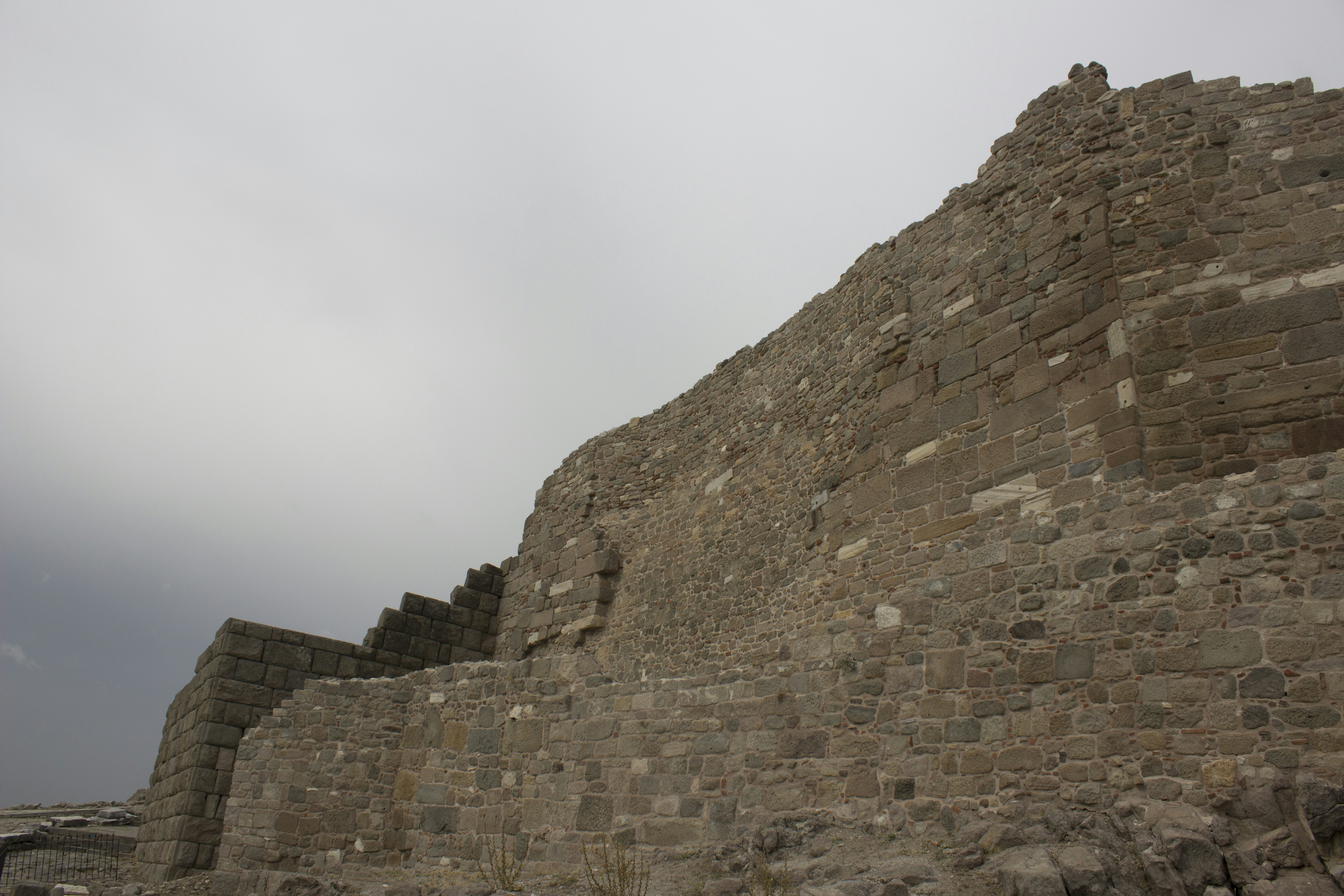 Weathered stone wall of an ancient fort beneath a cloudy sky.