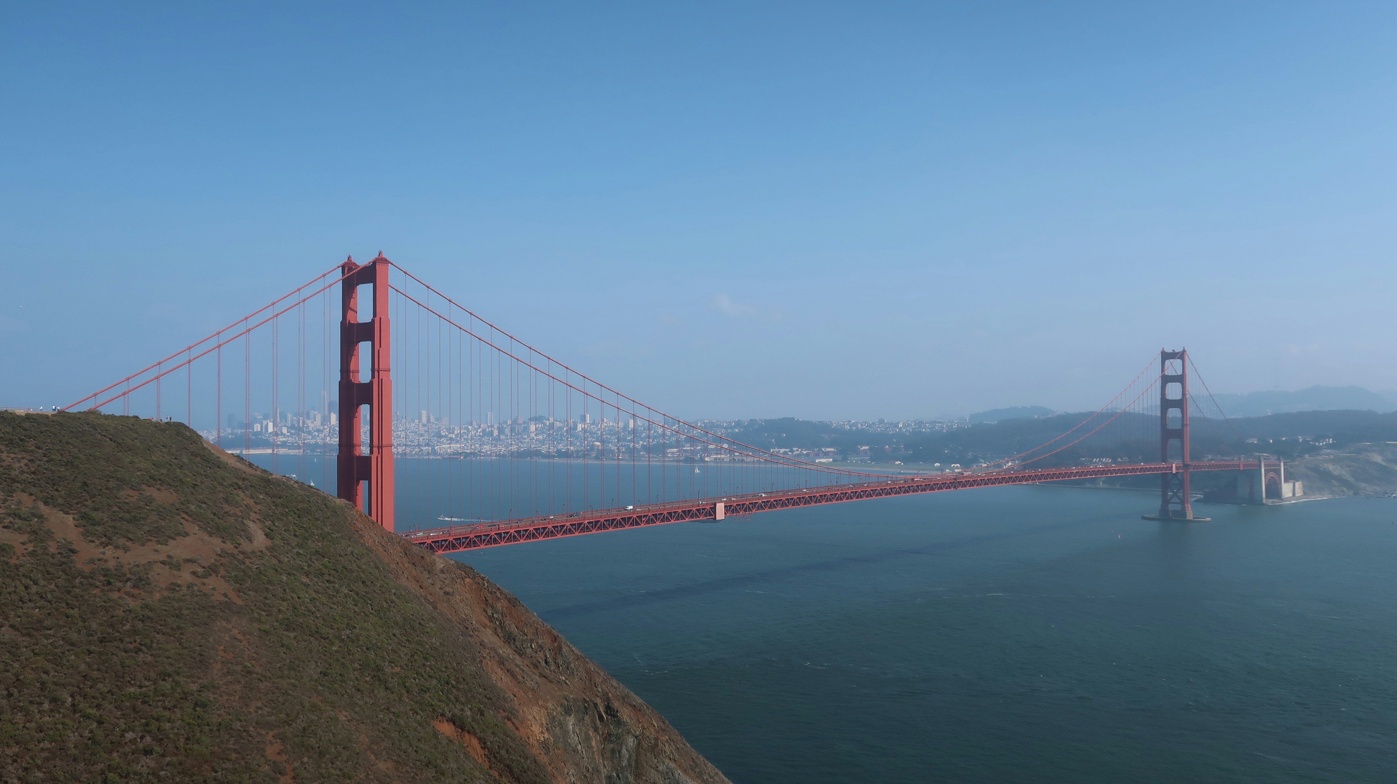 Golden Gate Bridge stretching over the bay, framed by rolling hills and a clear blue sky.
