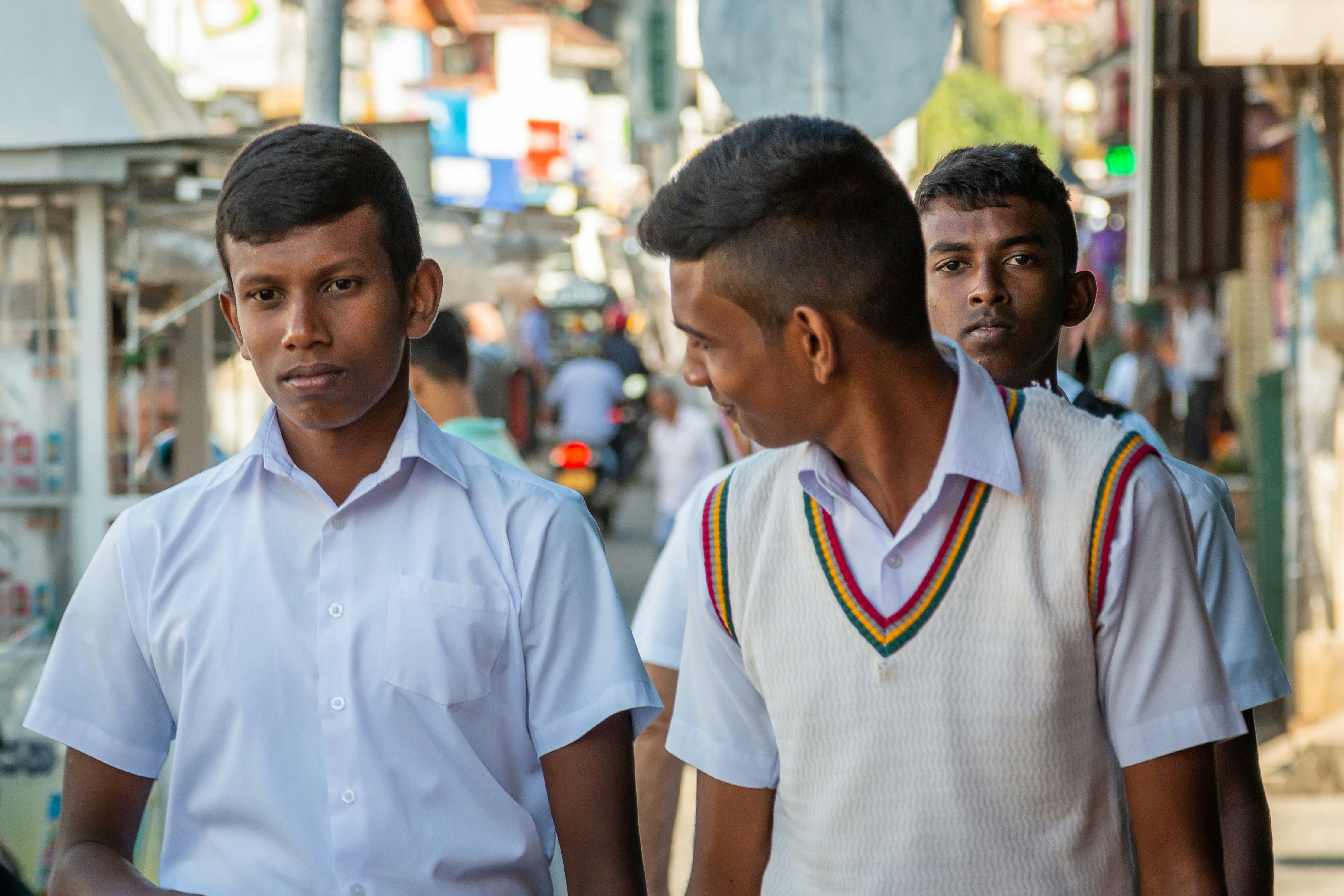Three young men in school uniforms strolling through a bustling street, engaged in conversation amidst a vibrant urban backdrop.