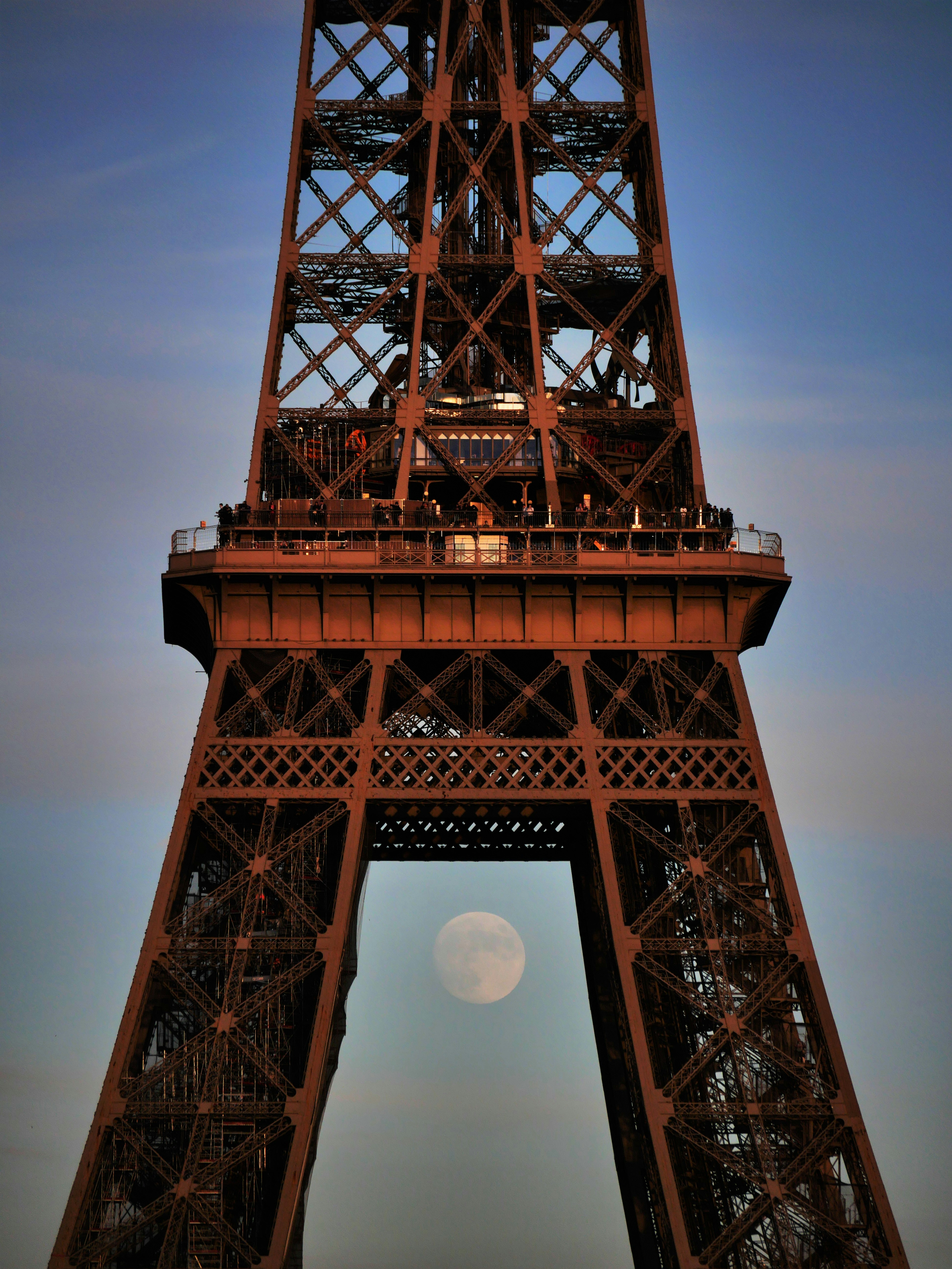 The Eiffel Tower's intricate ironwork frames a serene full moon against a twilight sky.