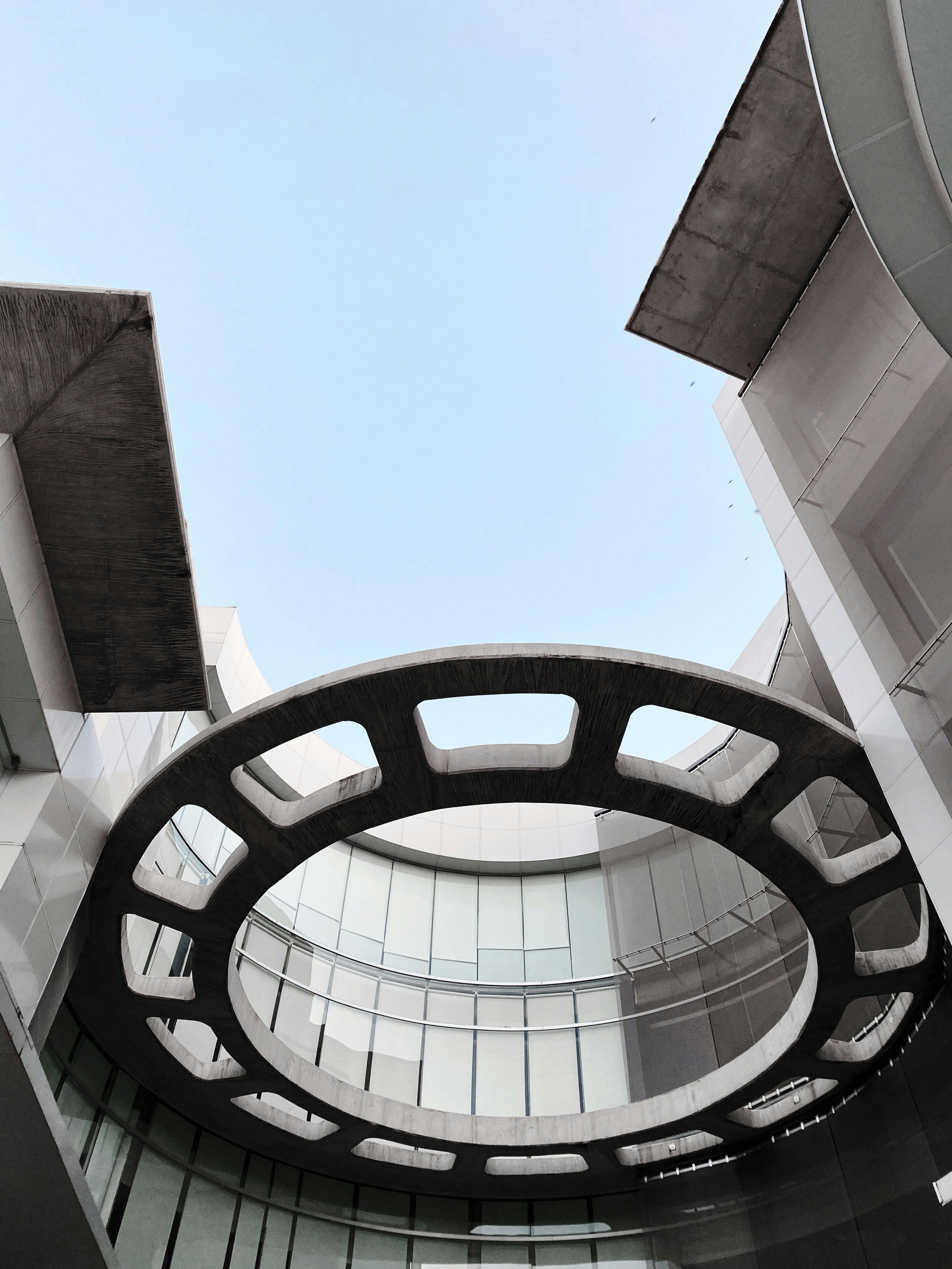Circular architectural structure framed by modern buildings against a clear blue sky.