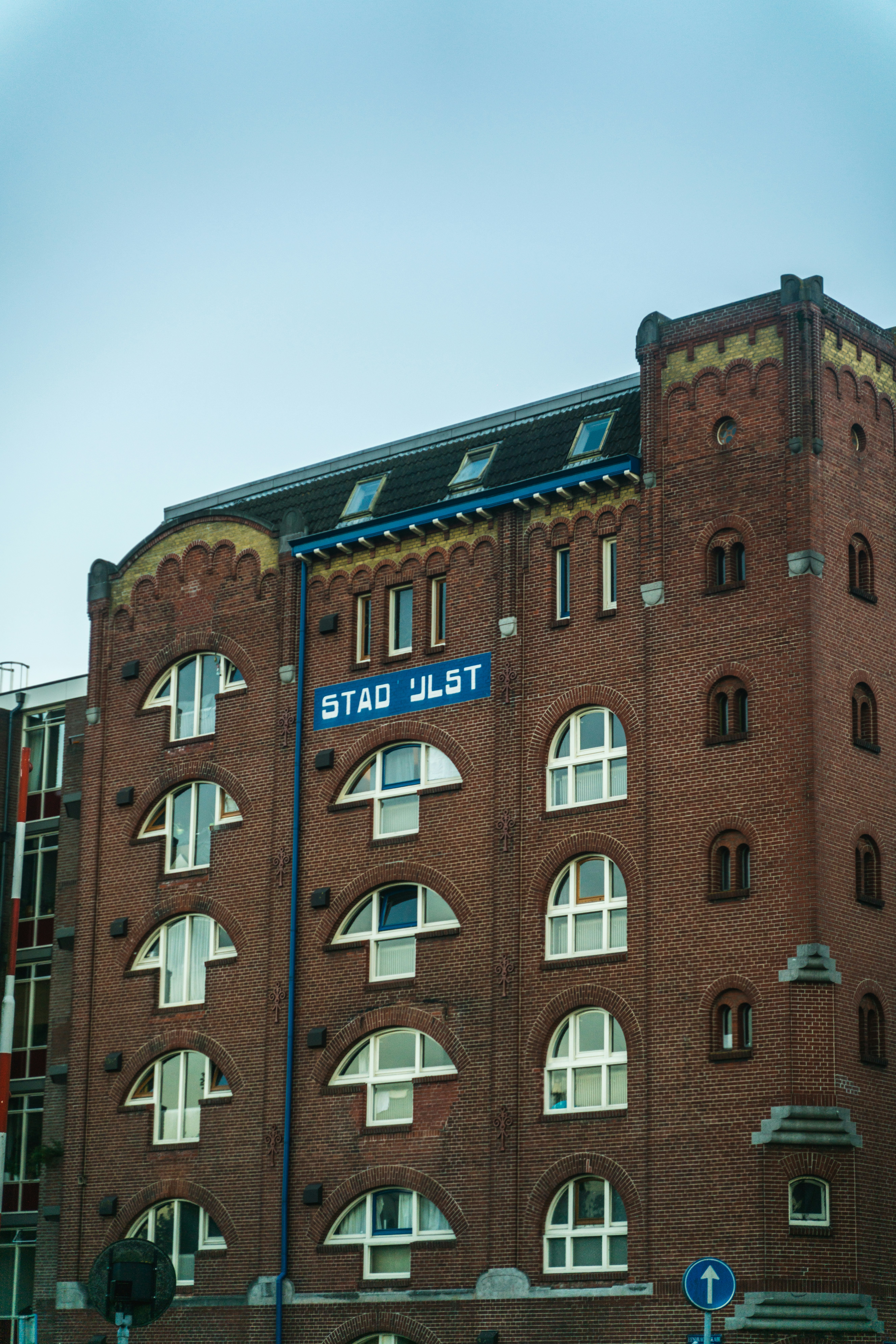 Brick building featuring arched windows and a prominent blue sign reading 'STAD JULST.'