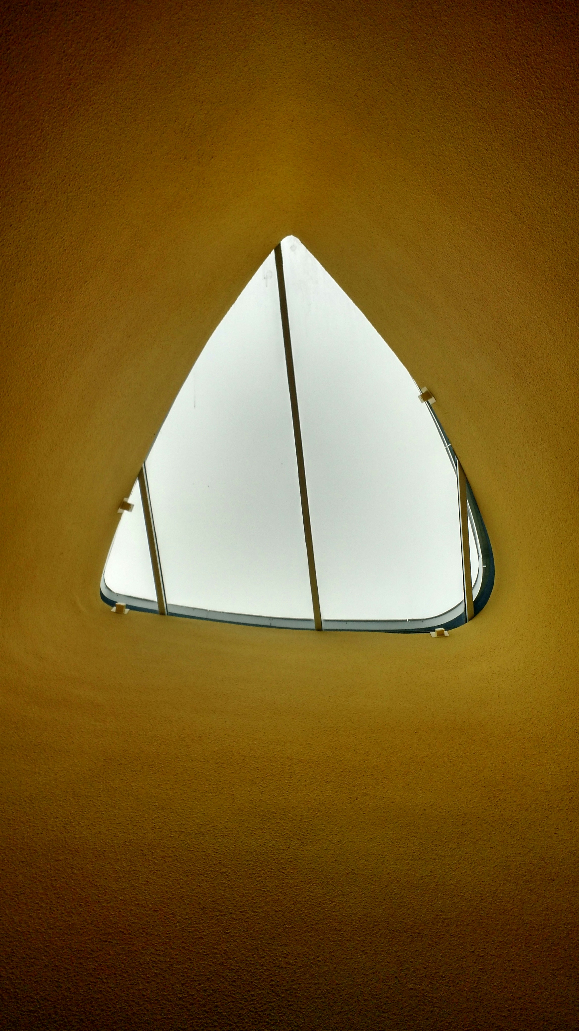 Triangular skylight framed by textured yellow walls, providing a unique view of the sky above.