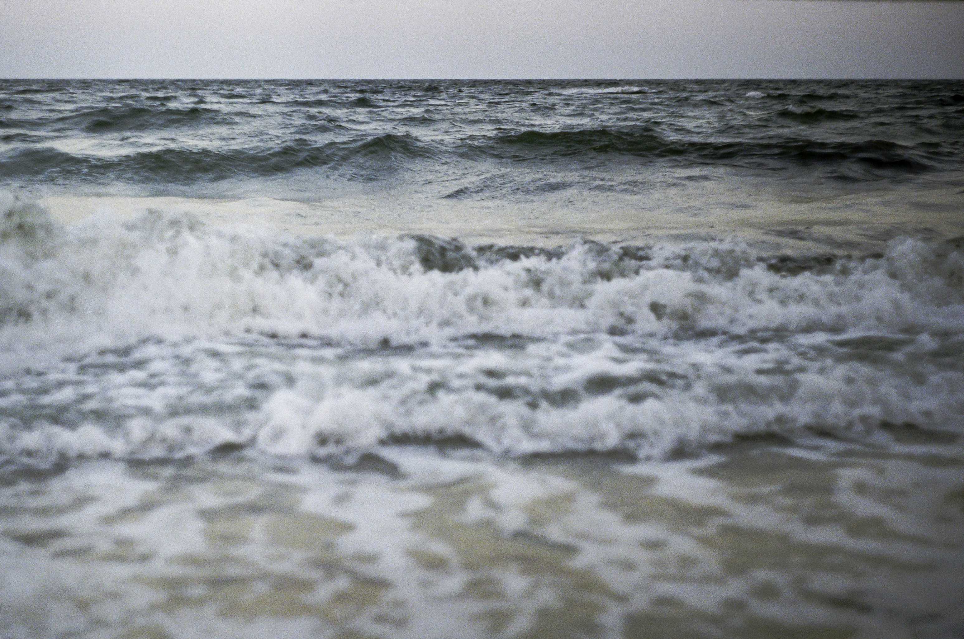 Waves crash onto a sandy beach under a cloudy October sky.