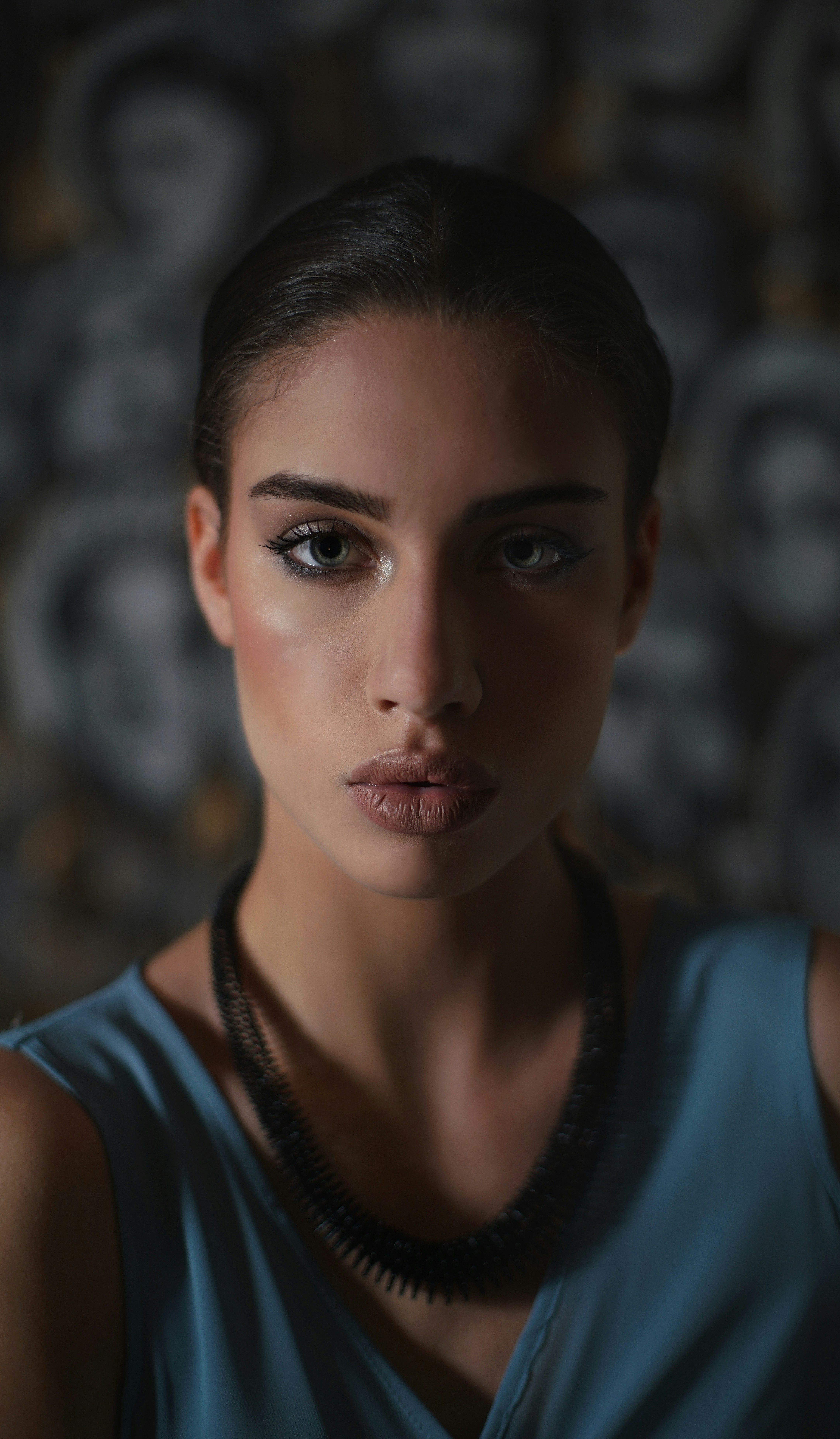 Close-up portrait of a woman with striking features, wearing a dark necklace against a softly blurred background.