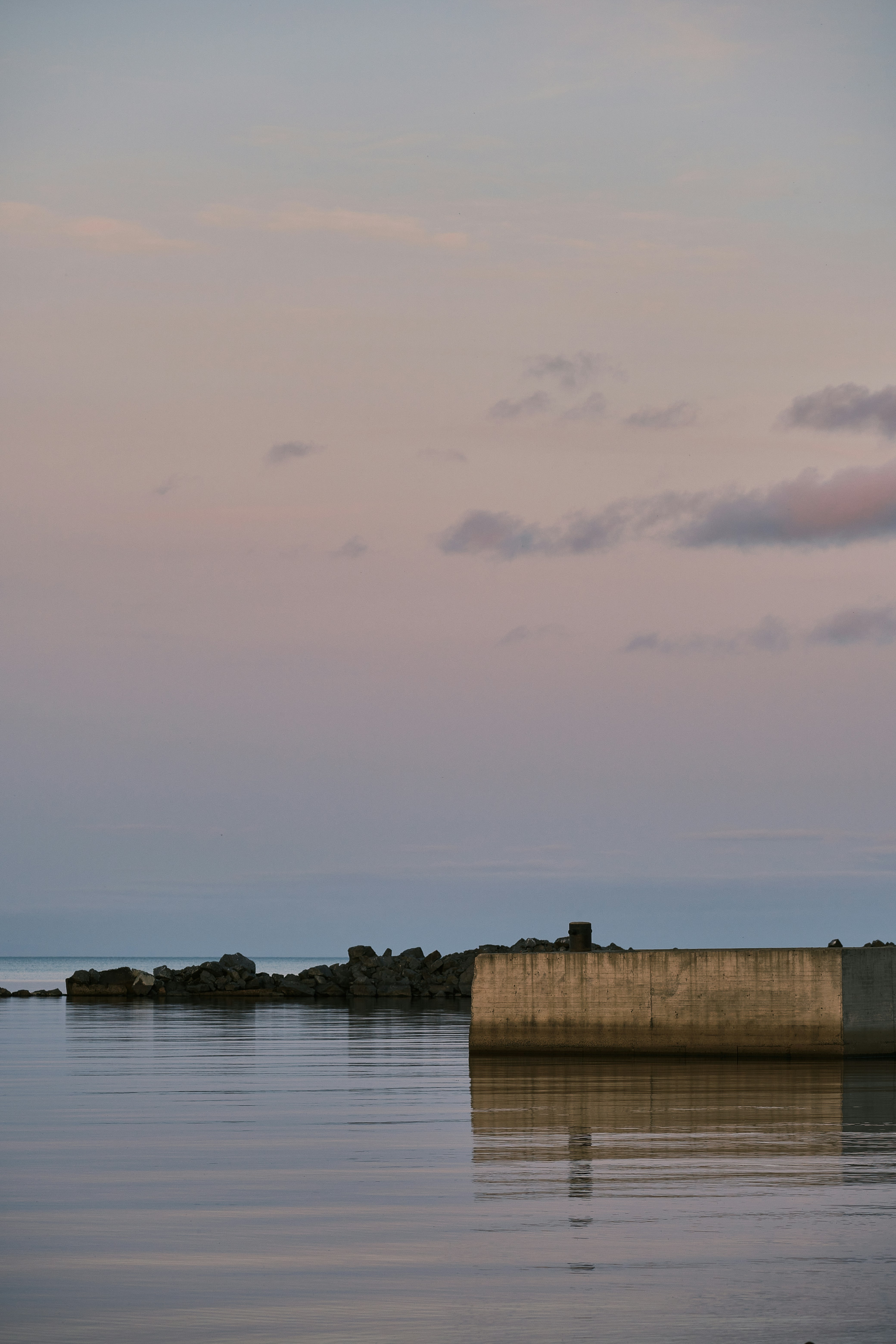 Harbor at Dusk: A Concrete Breakwater Embraced by Soft Pink Light