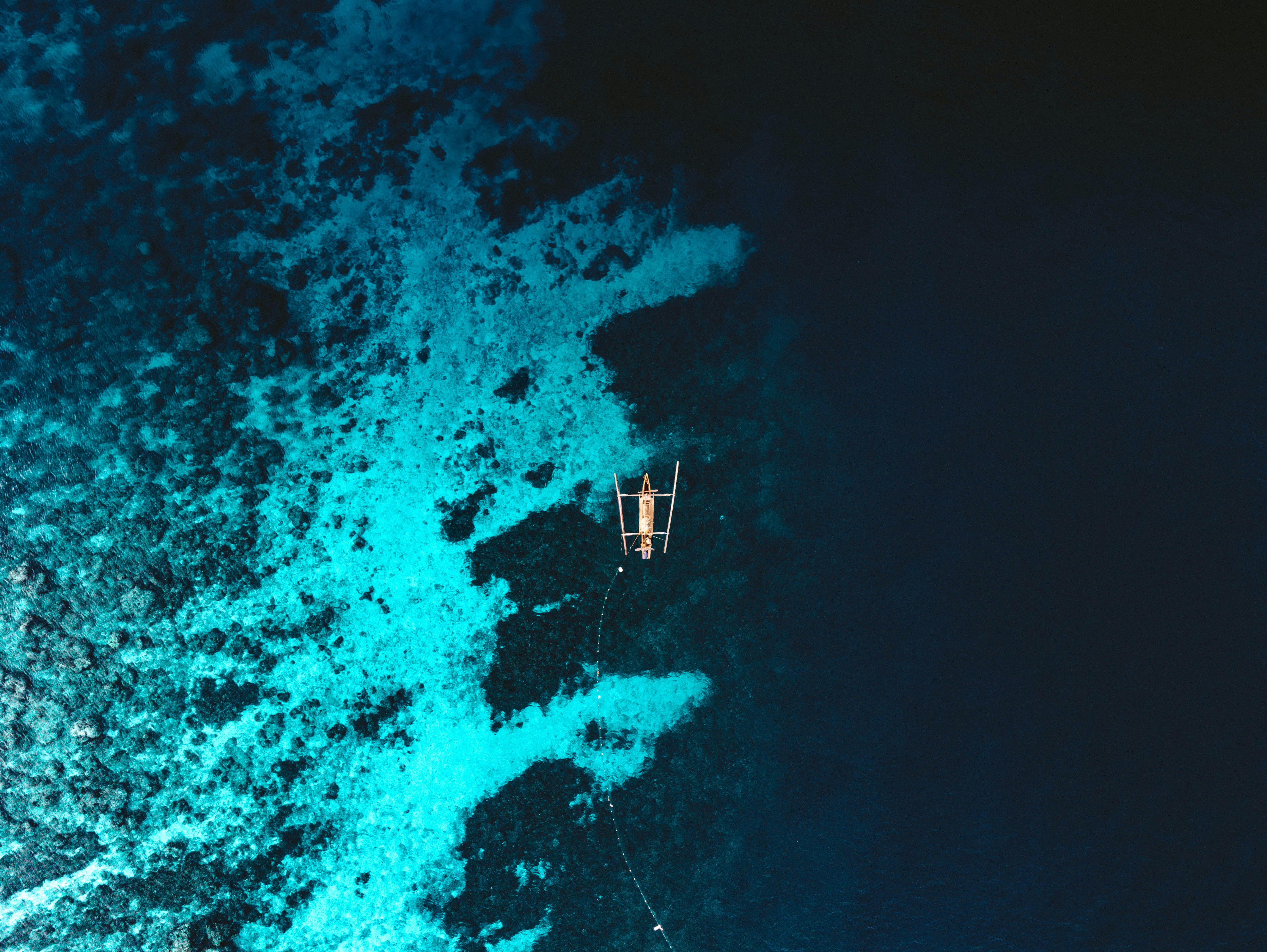 A lone boat navigates the vibrant turquoise waters, revealing the intricate patterns of the coral below. The deep blue contrasts beautifully with the lighter hues of the sea.
