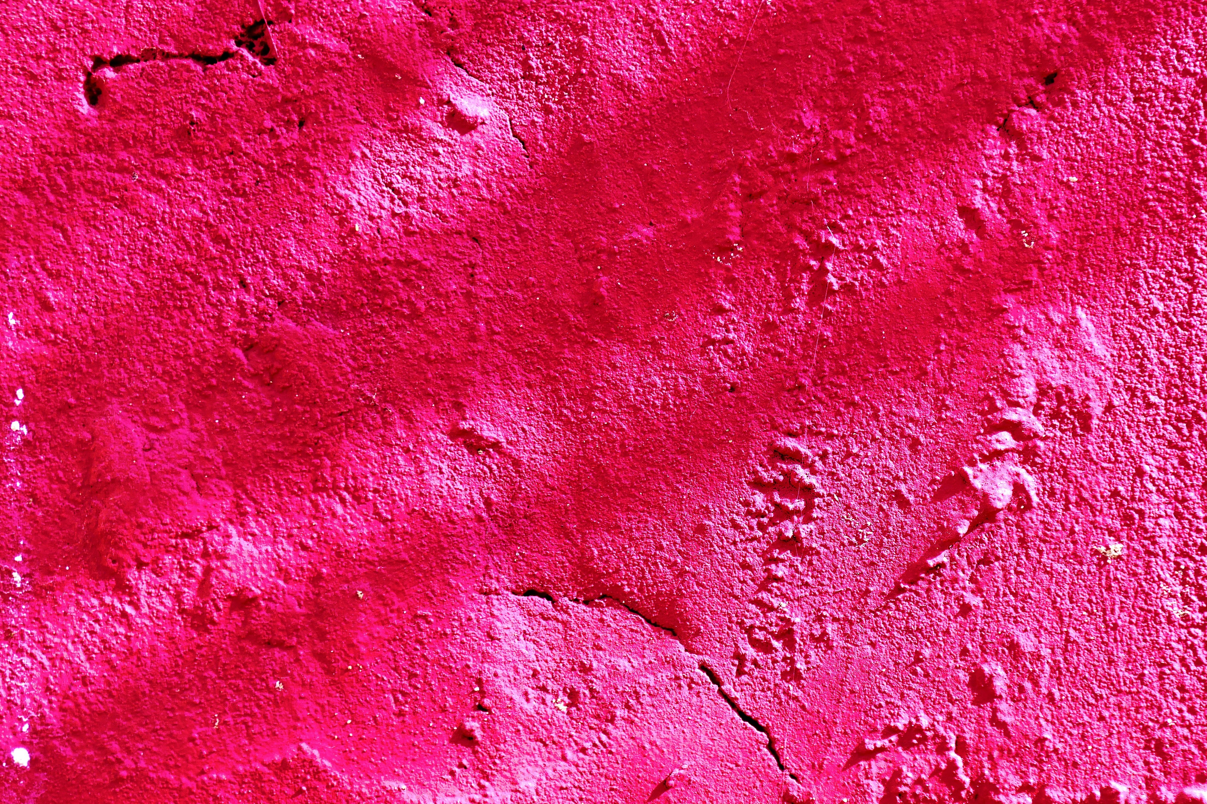 Close-up of a vibrant pink wall showcasing unique textures and cracks, highlighting the passage of time and urban art.