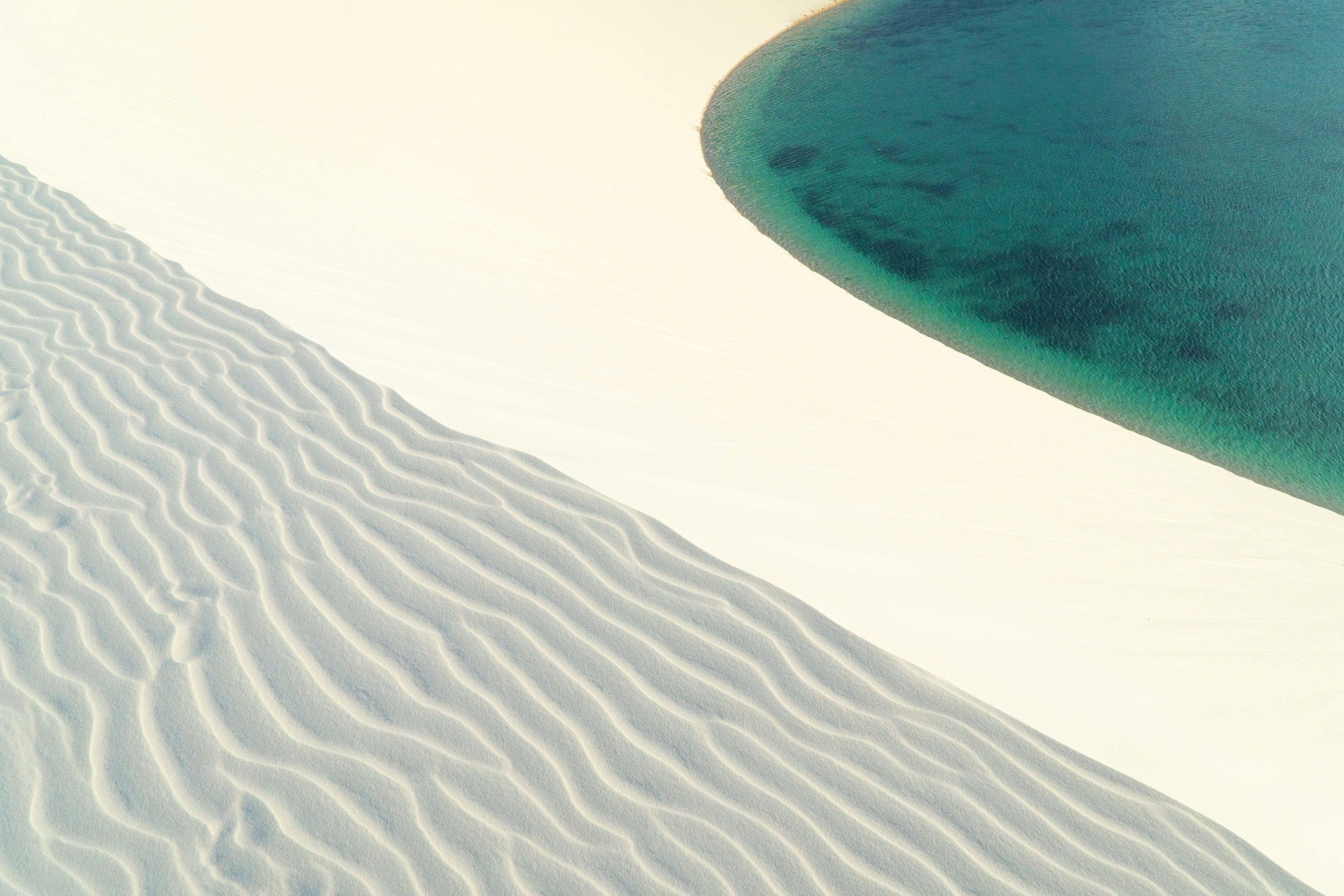 Textured white sand dunes curve alongside a serene turquoise lagoon, showcasing the harmony of land and water.