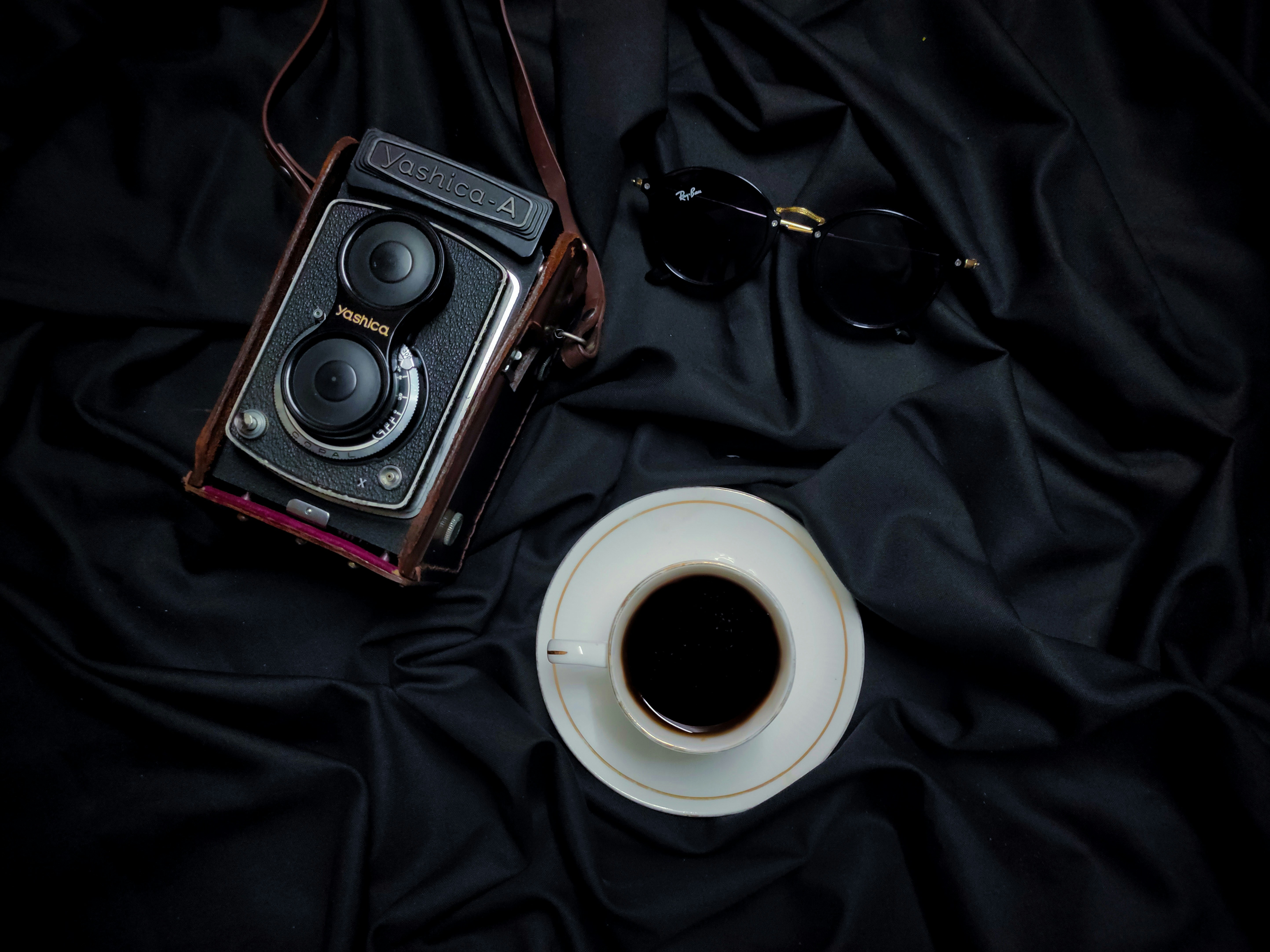 Black and silver dslr camera beside white ceramic mug on black textile ...