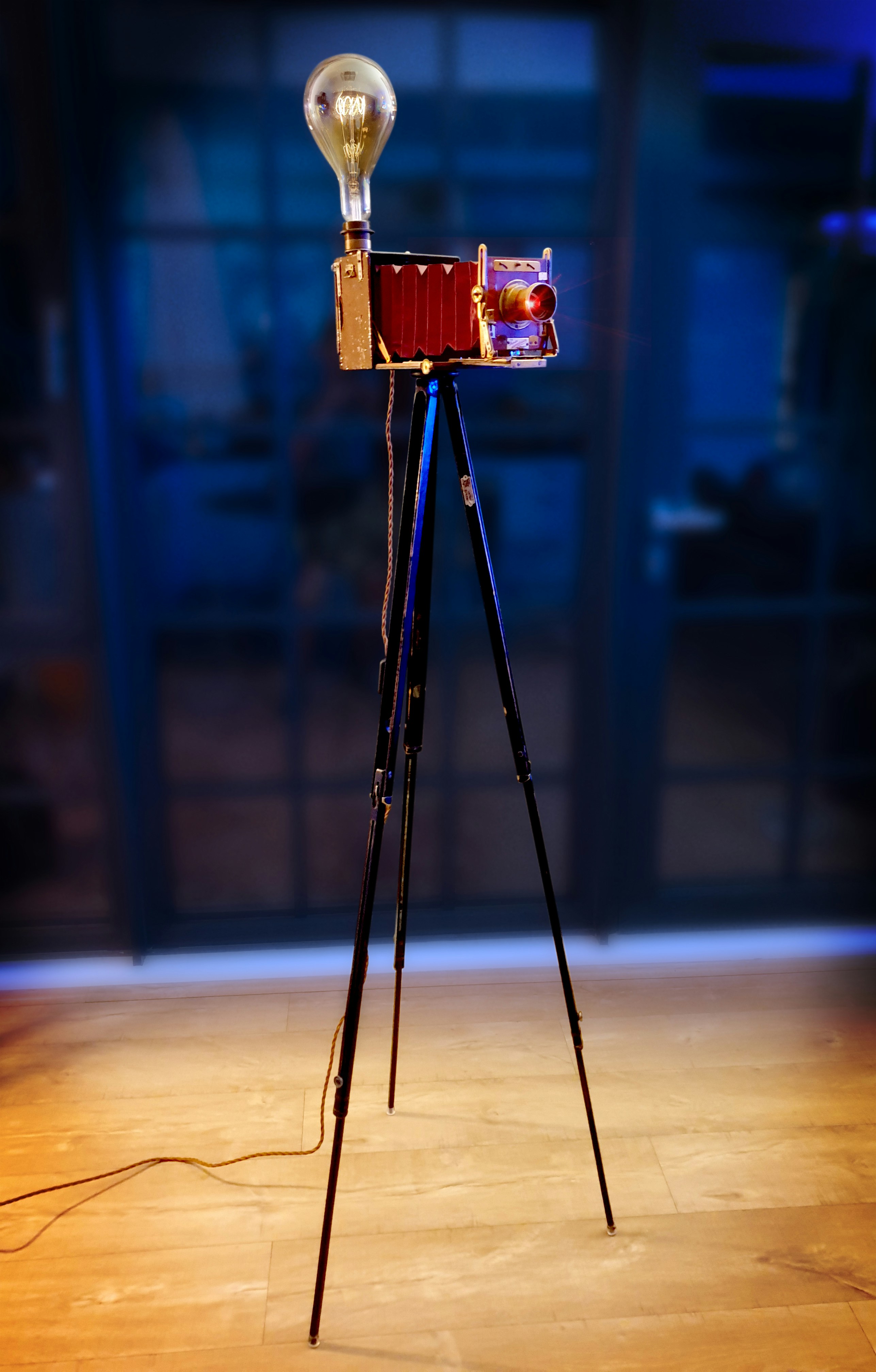 Antique camera setup with a light bulb on top, standing on a tripod against a softly lit background.