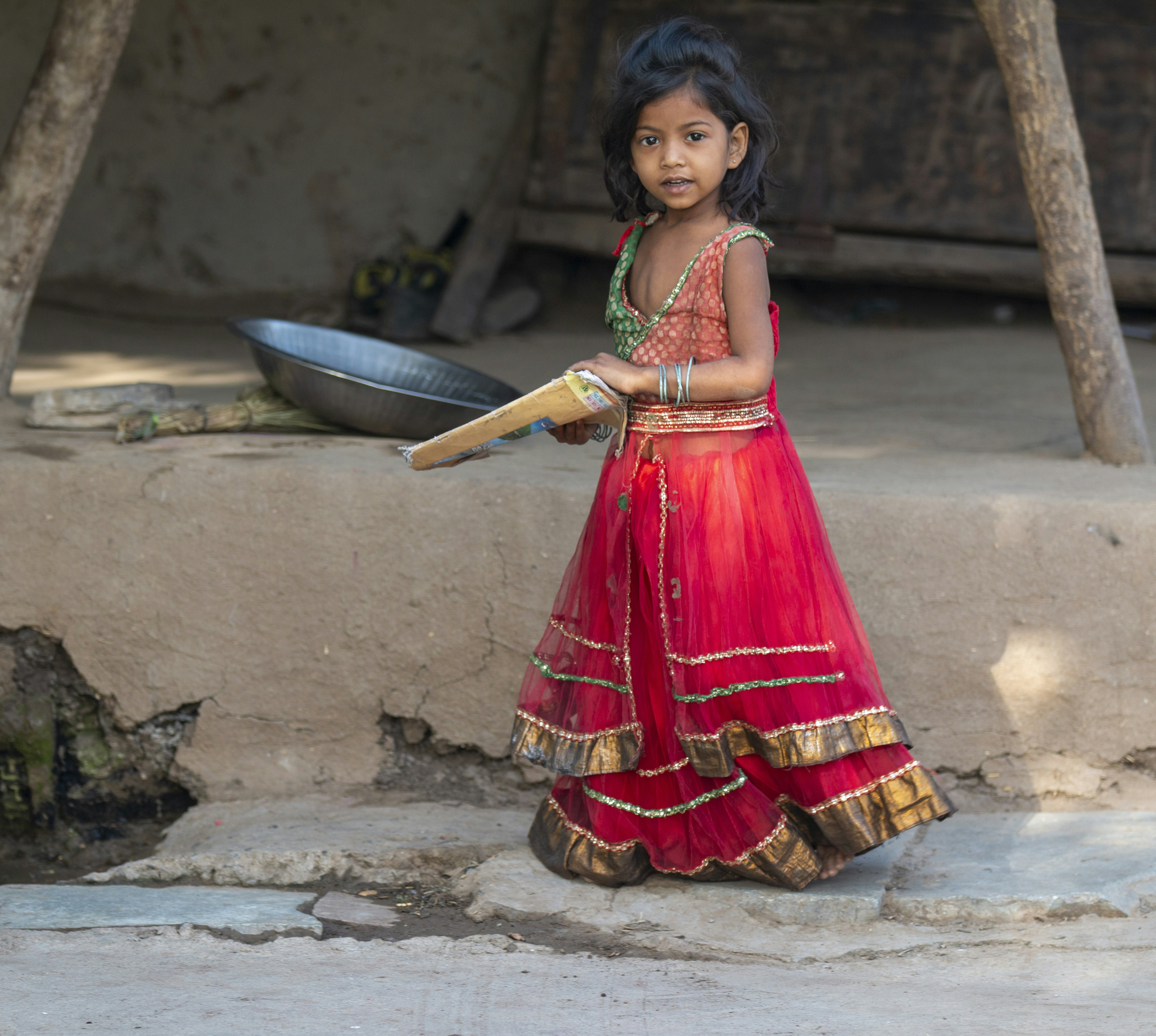 Crimson Courtyard, Quiet Strength: a village girl in festive attire with a wooden tool