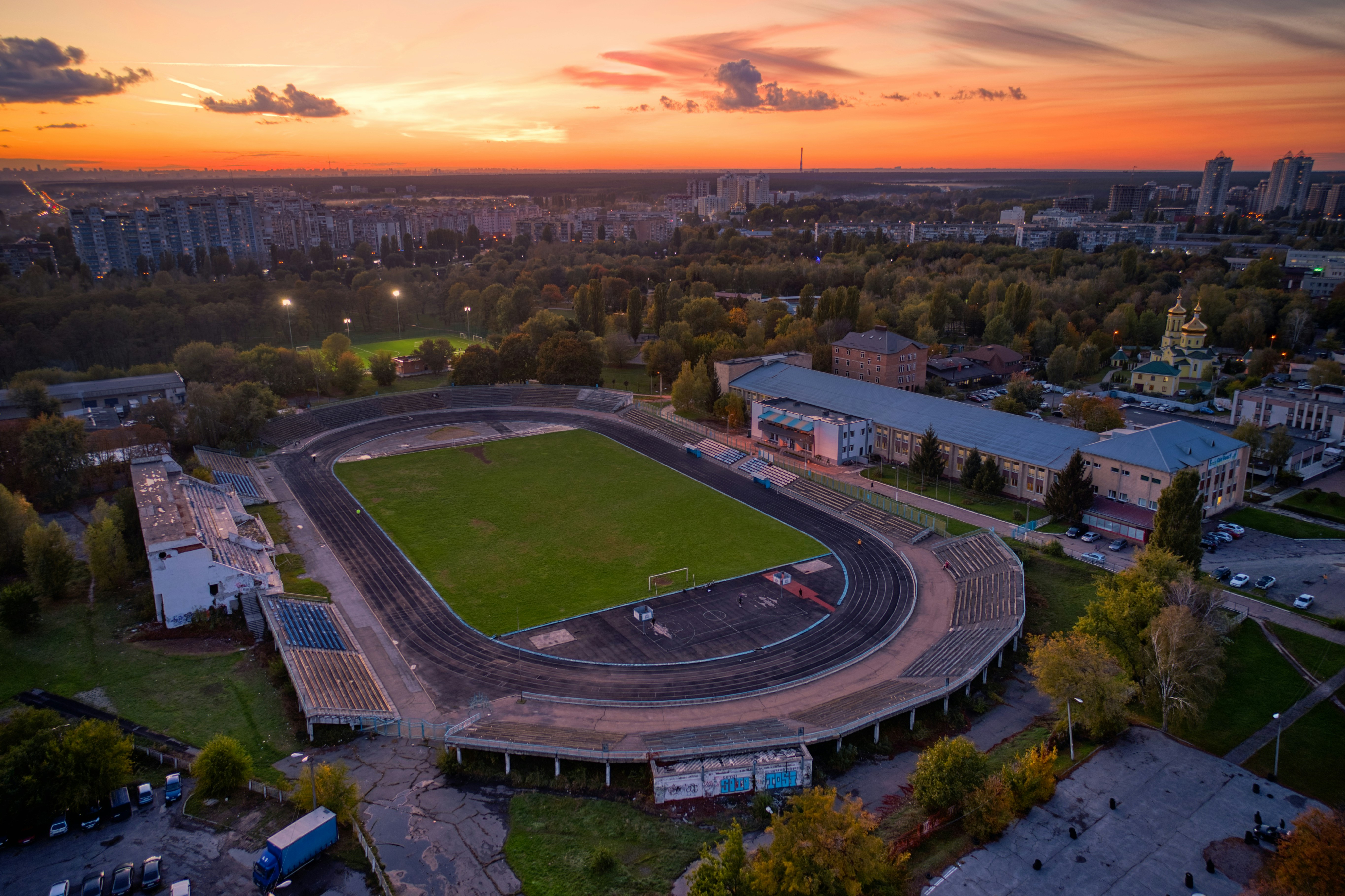 Aerial view of Spartak Stadium surrounded by lush greenery and urban landscape at sunset.