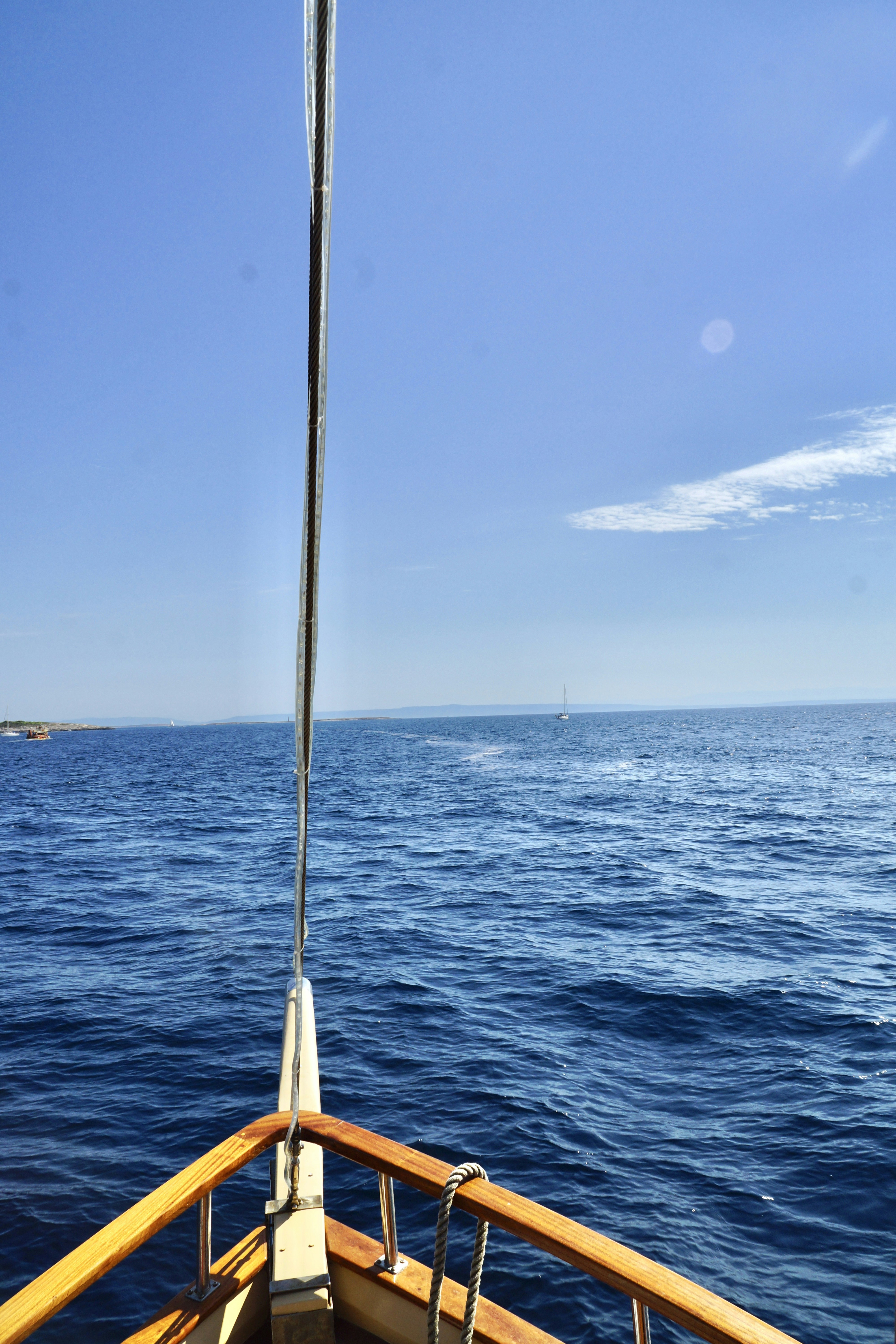 Bow of a wooden sailboat cutting through deep blue sea under a clear sky.
