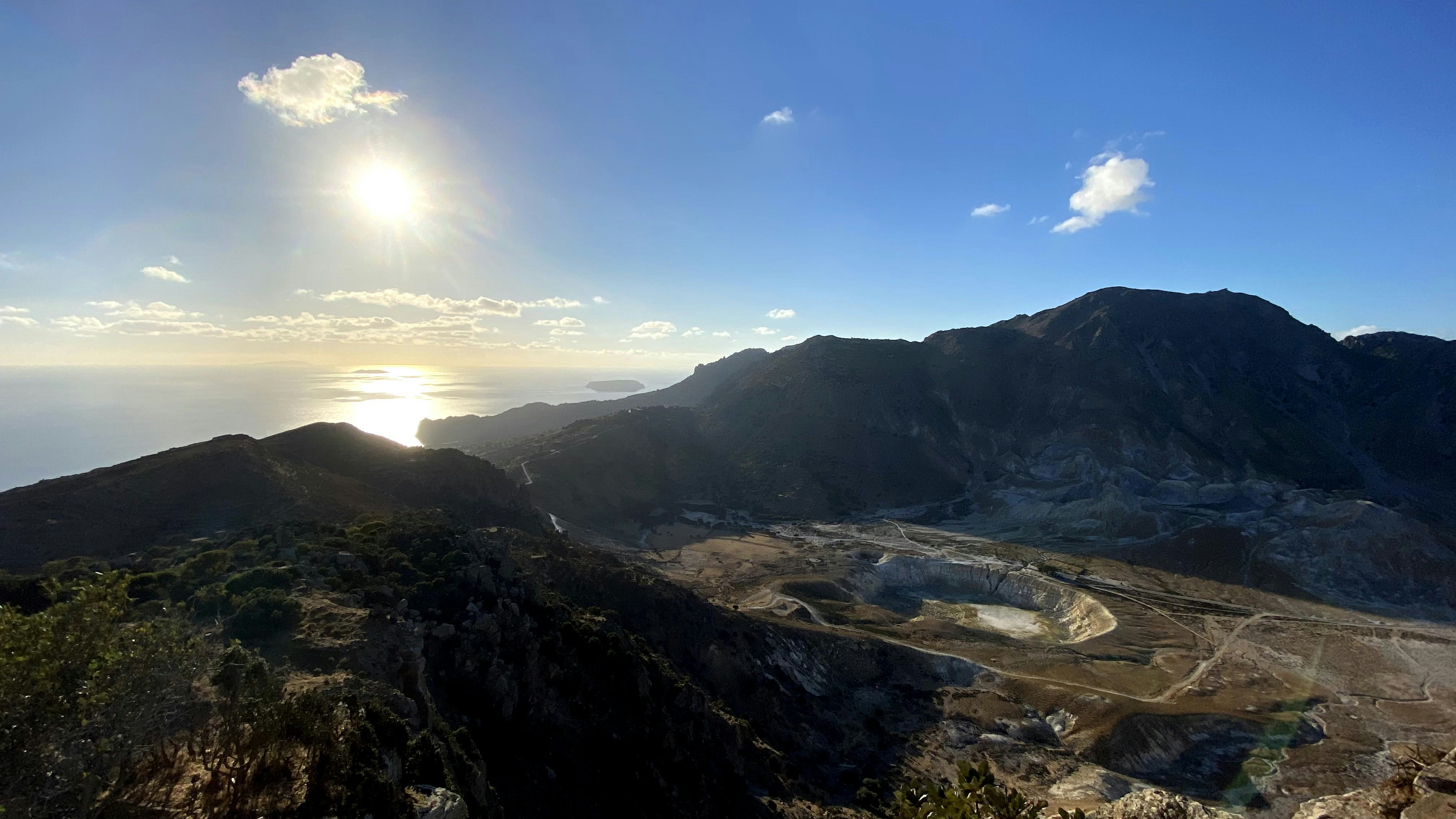 Nisyros island's volcanic caldera with rugged terrain under a bright sun and clear blue sky.