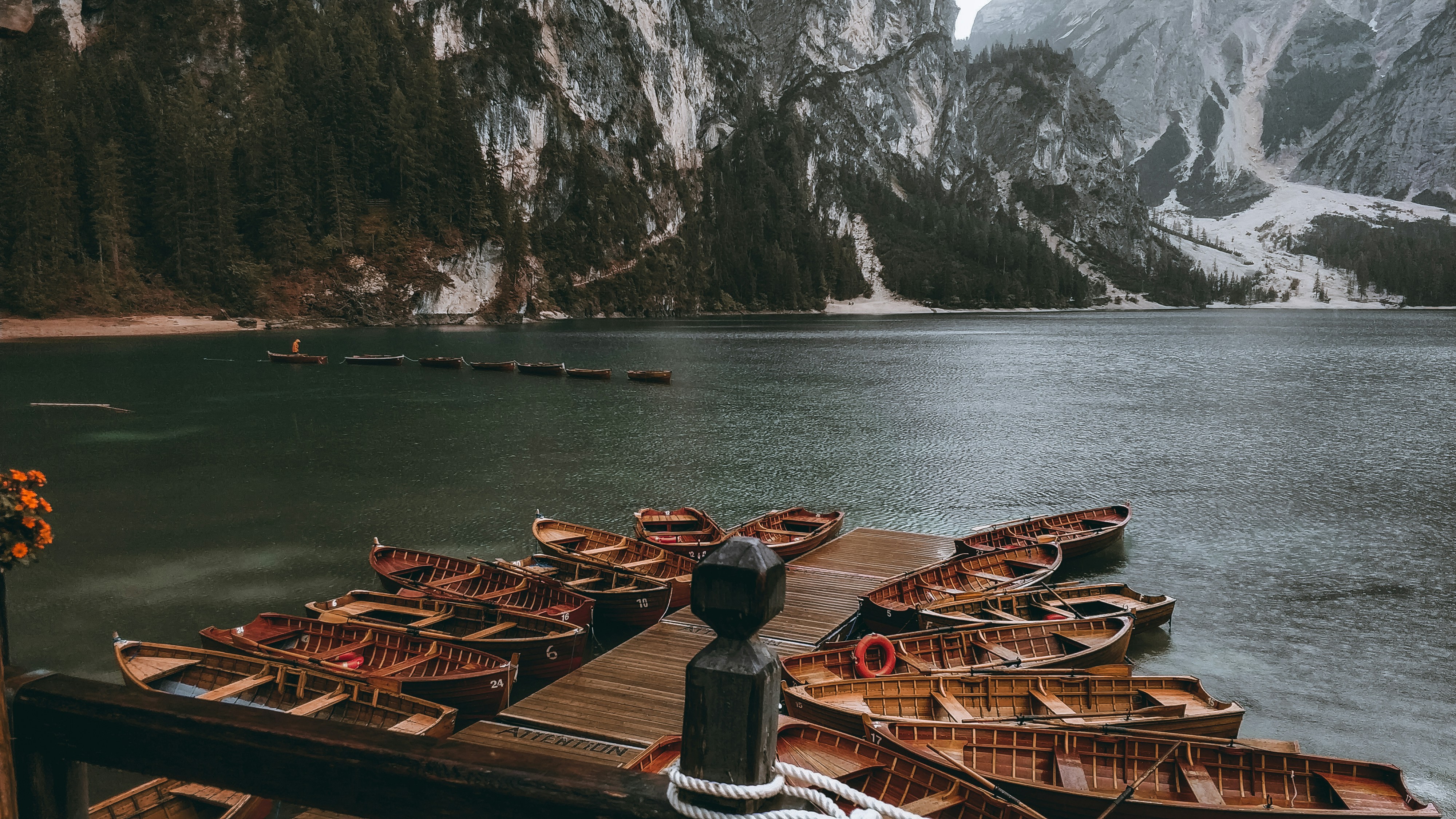 Wooden boats moored at a serene lake surrounded by towering mountains and lush forests. The scene reflects a peaceful coexistence of nature and human craftsmanship.