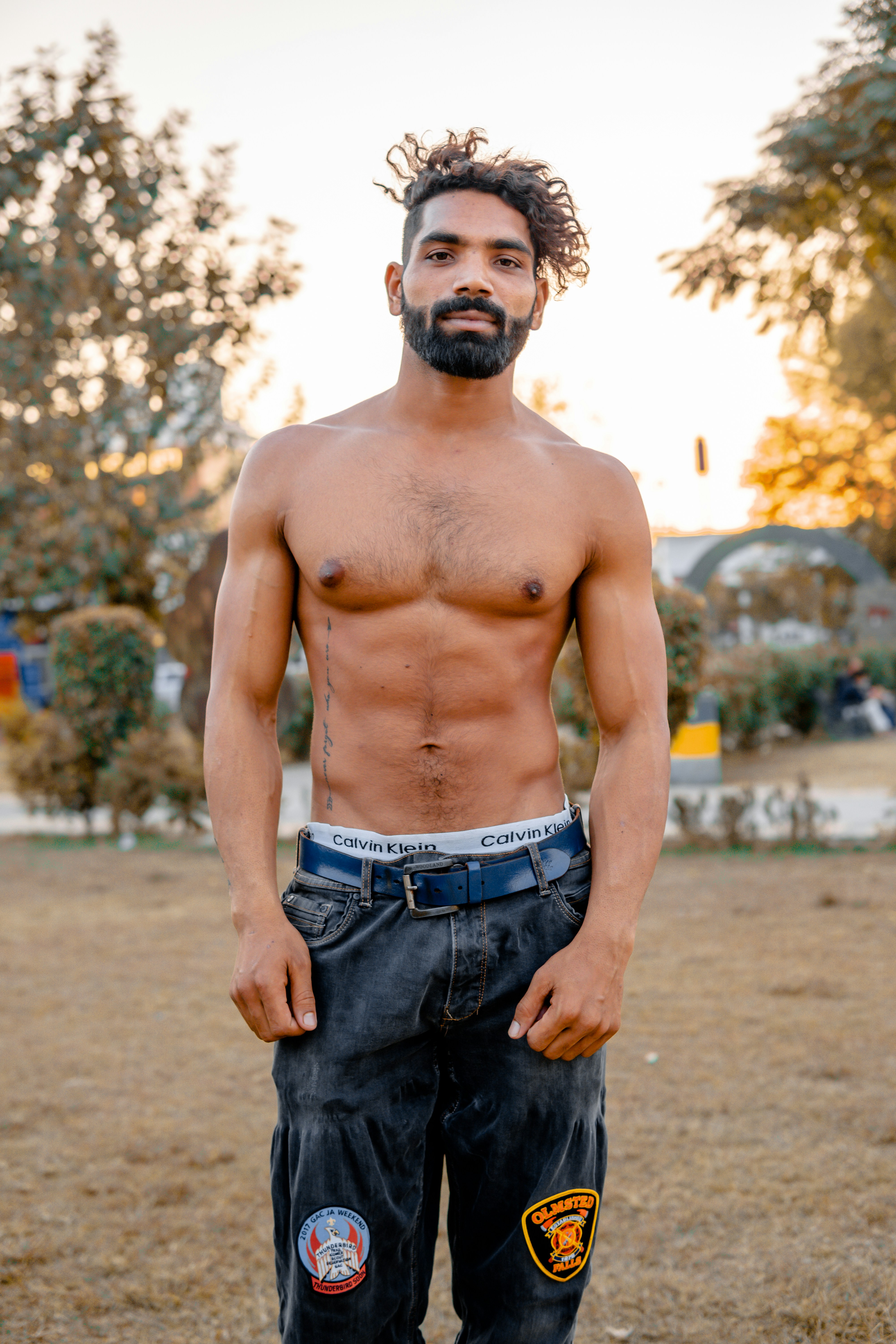 Topless Man In Blue Denim Jeans Standing Near Trees During Daytime