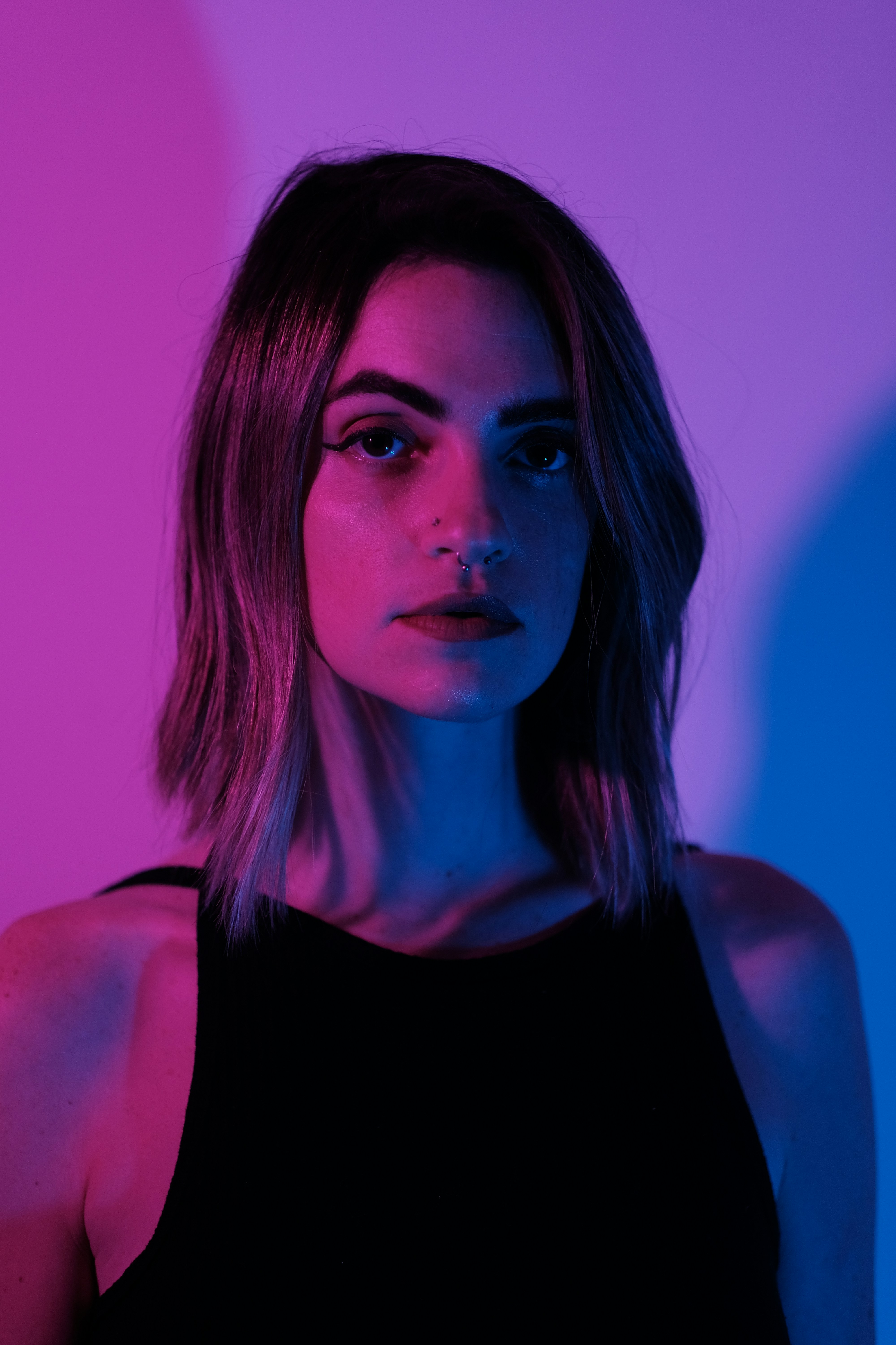 Portrait of a woman illuminated by vibrant pink and blue lighting, creating a striking contrast against a softly blurred background.
