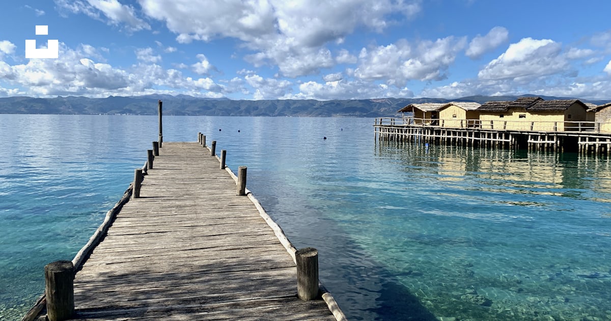 昼間の青と白の曇り空の下、青い海に浮かぶ茶色の木造船着き場の写真 Unsplashの無料オフリド写真